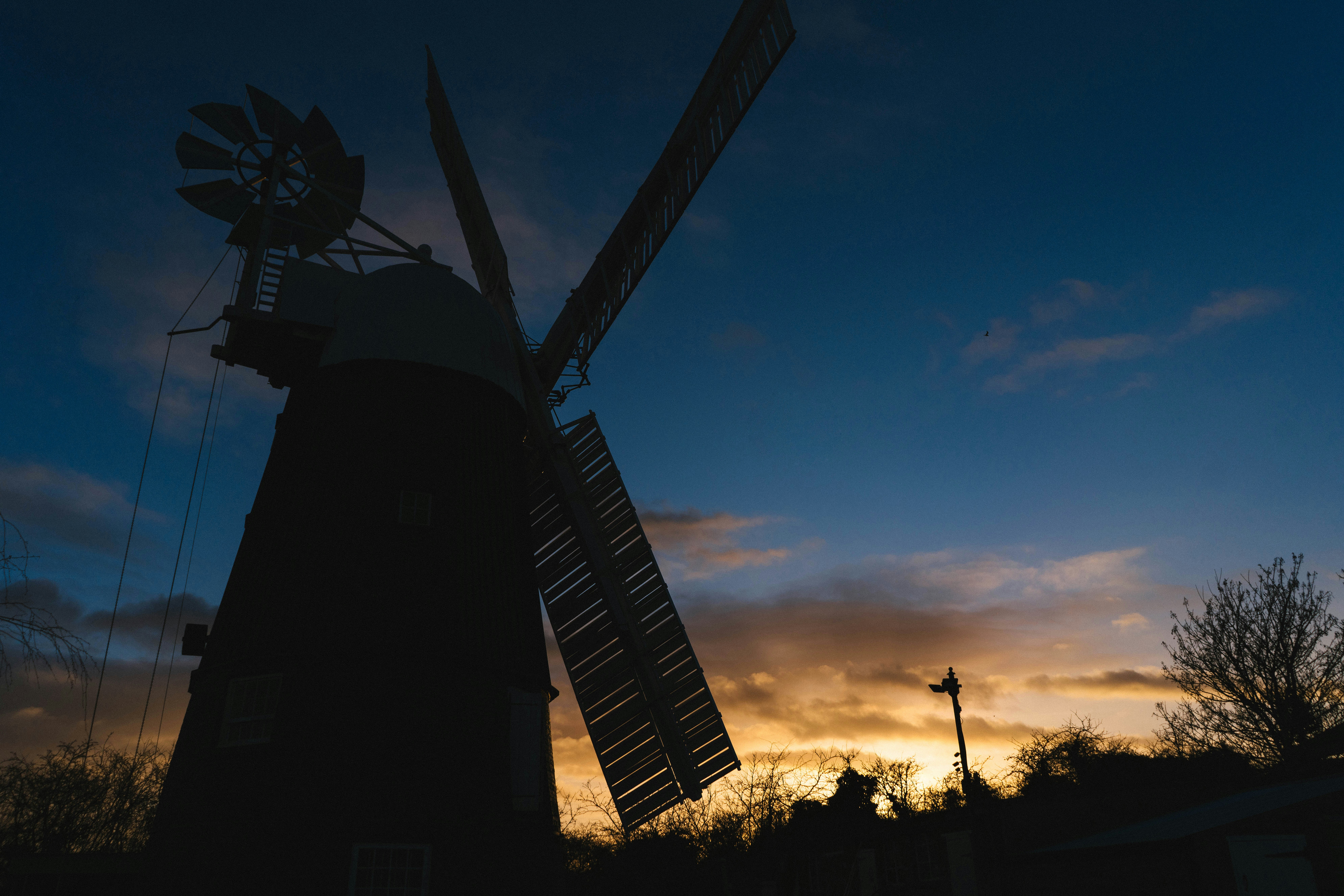 A windmill is silhouetted against the evening sky photo – Free Sunset ...