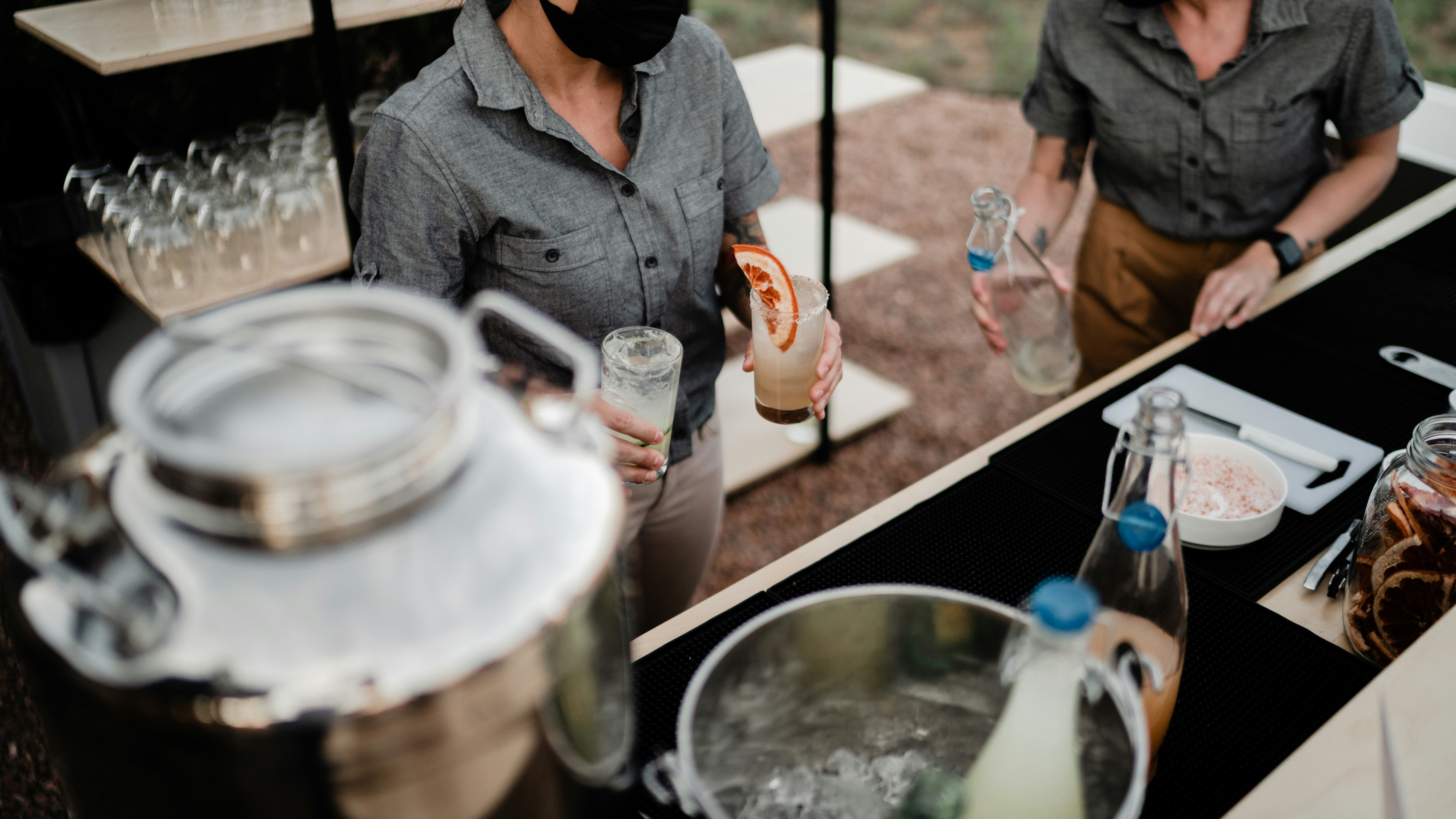 Two individuals prepare drinks at a stylish outdoor bar, showcasing a variety of beverages and garnishes.