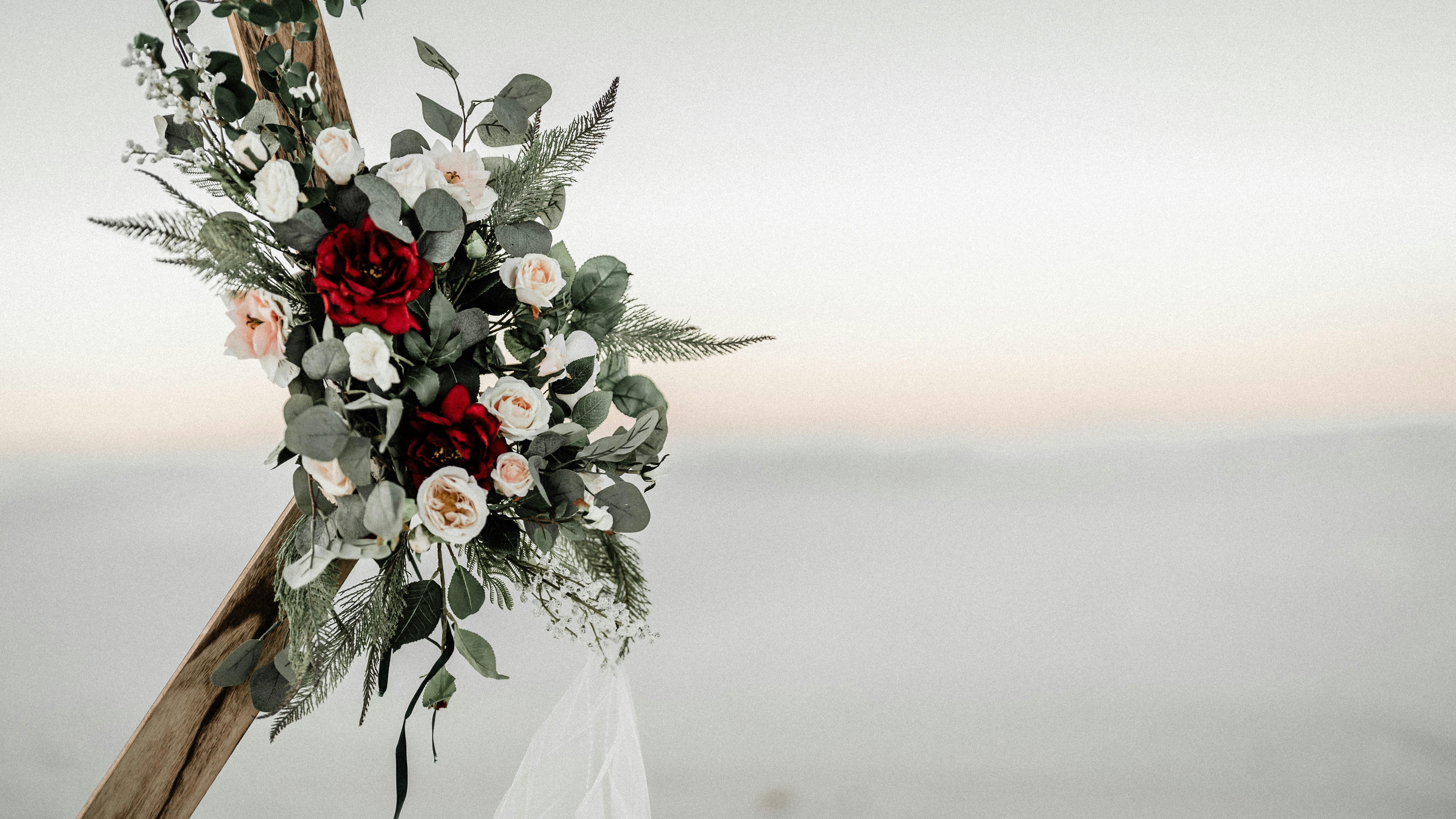 Floral arrangement featuring red and white roses intertwined with greenery, set against a soft, muted background.