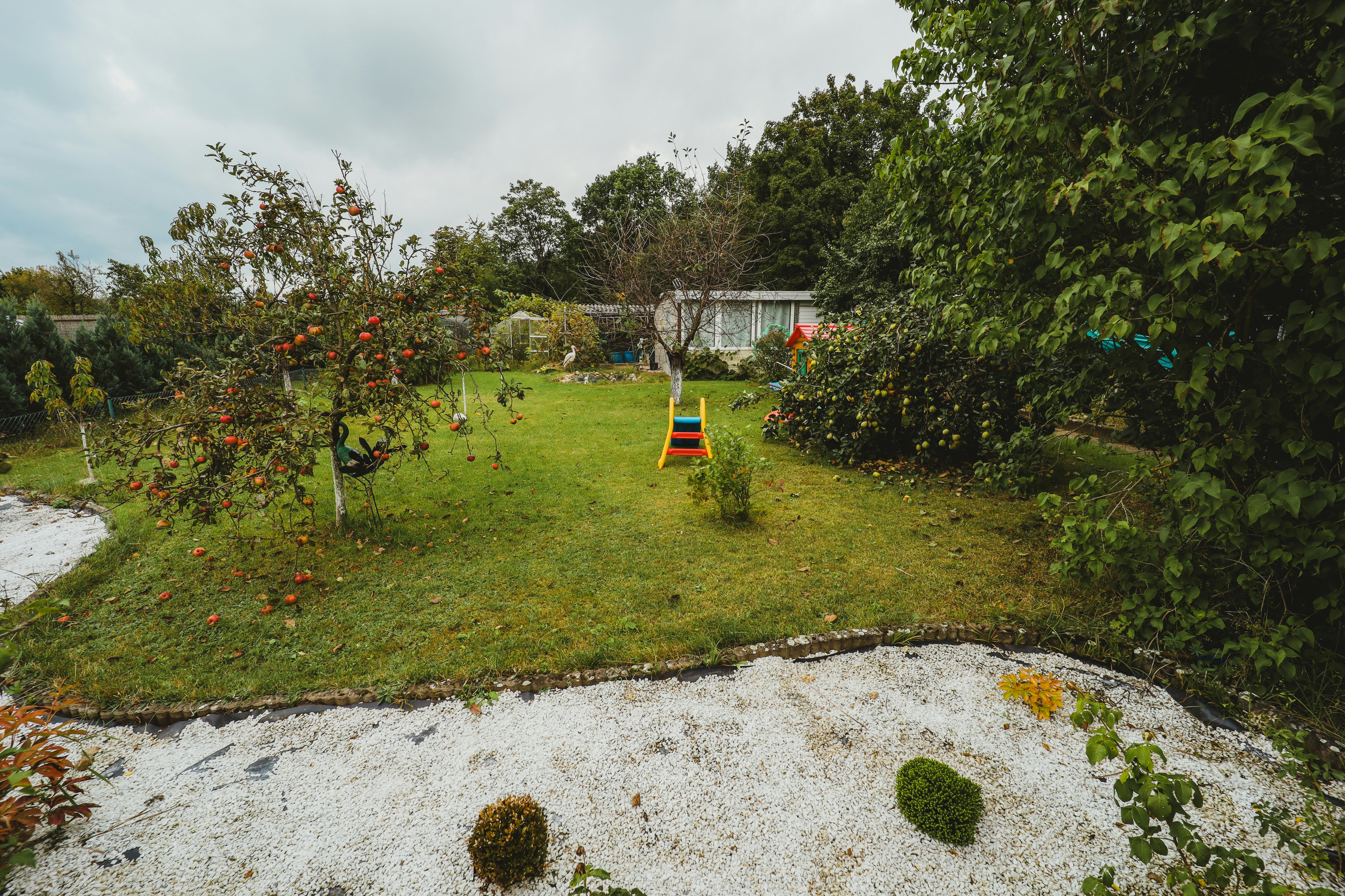A vibrant garden scene featuring lush greenery, fruit-bearing trees, and a colorful children's play structure, inviting exploration and relaxation.