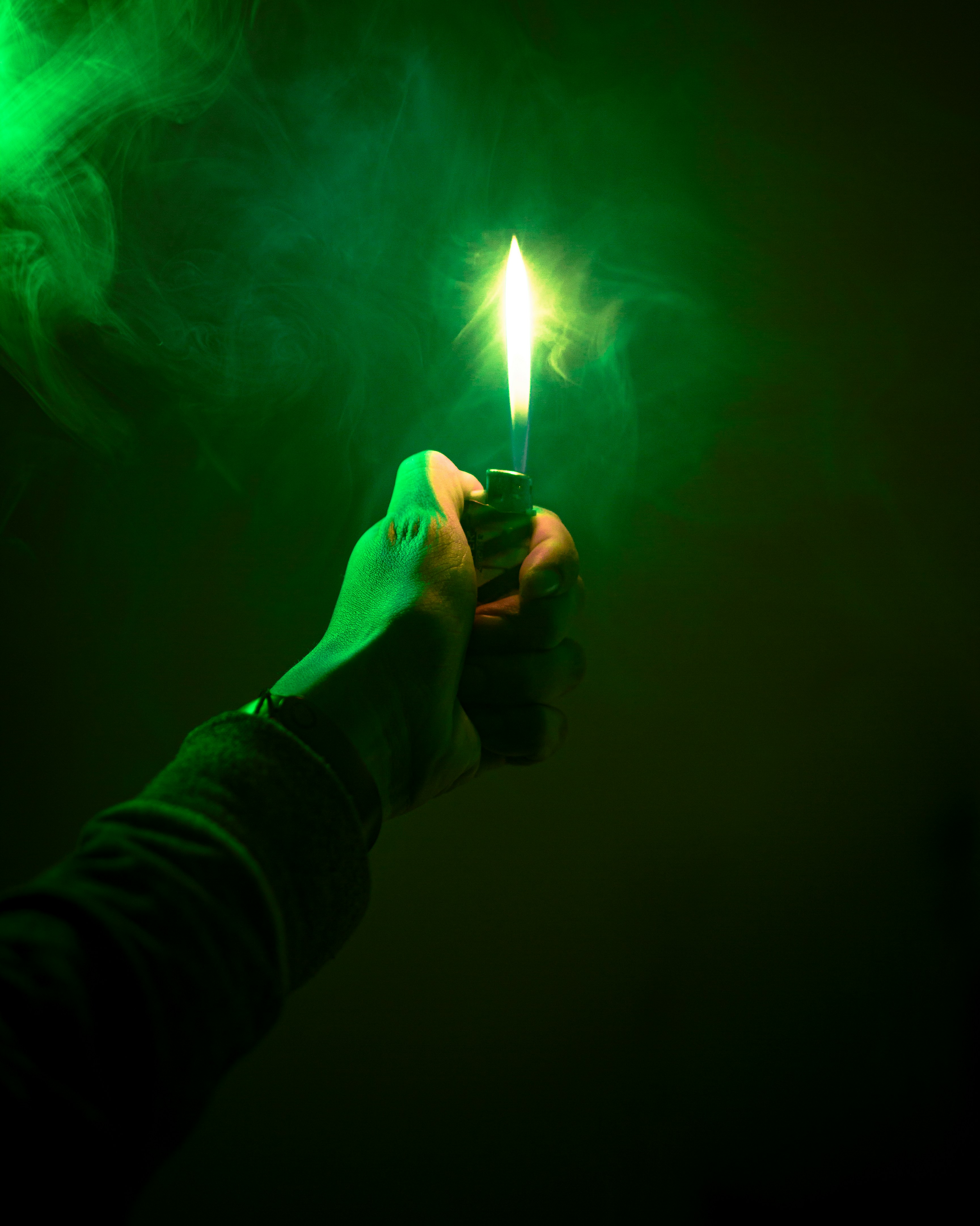 Green Flame: A Handheld Lighter Silhouette Against Neon Smoke
