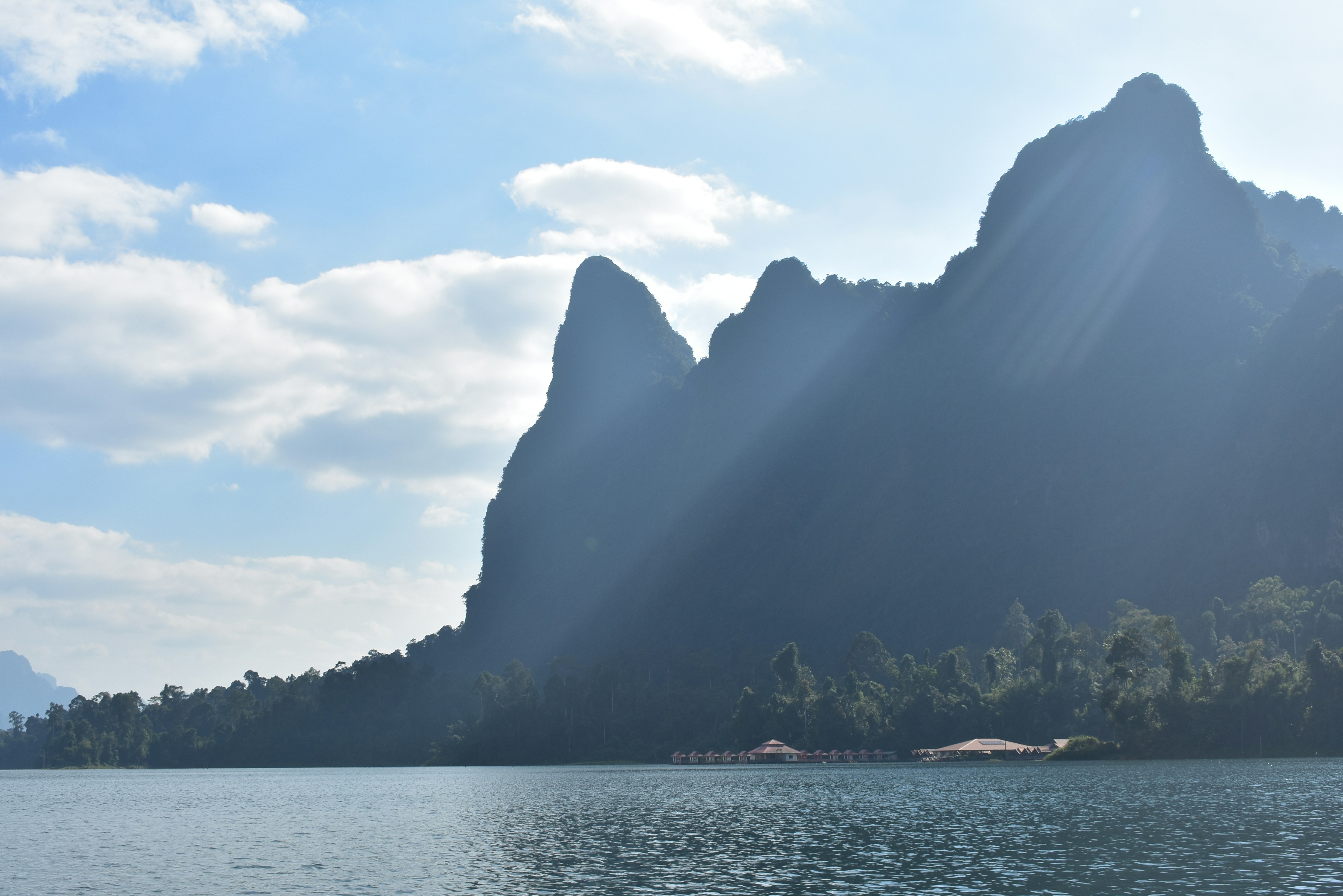 Dramatic mountain silhouette framed against a bright sky, with sunlight streaming over a calm lake.