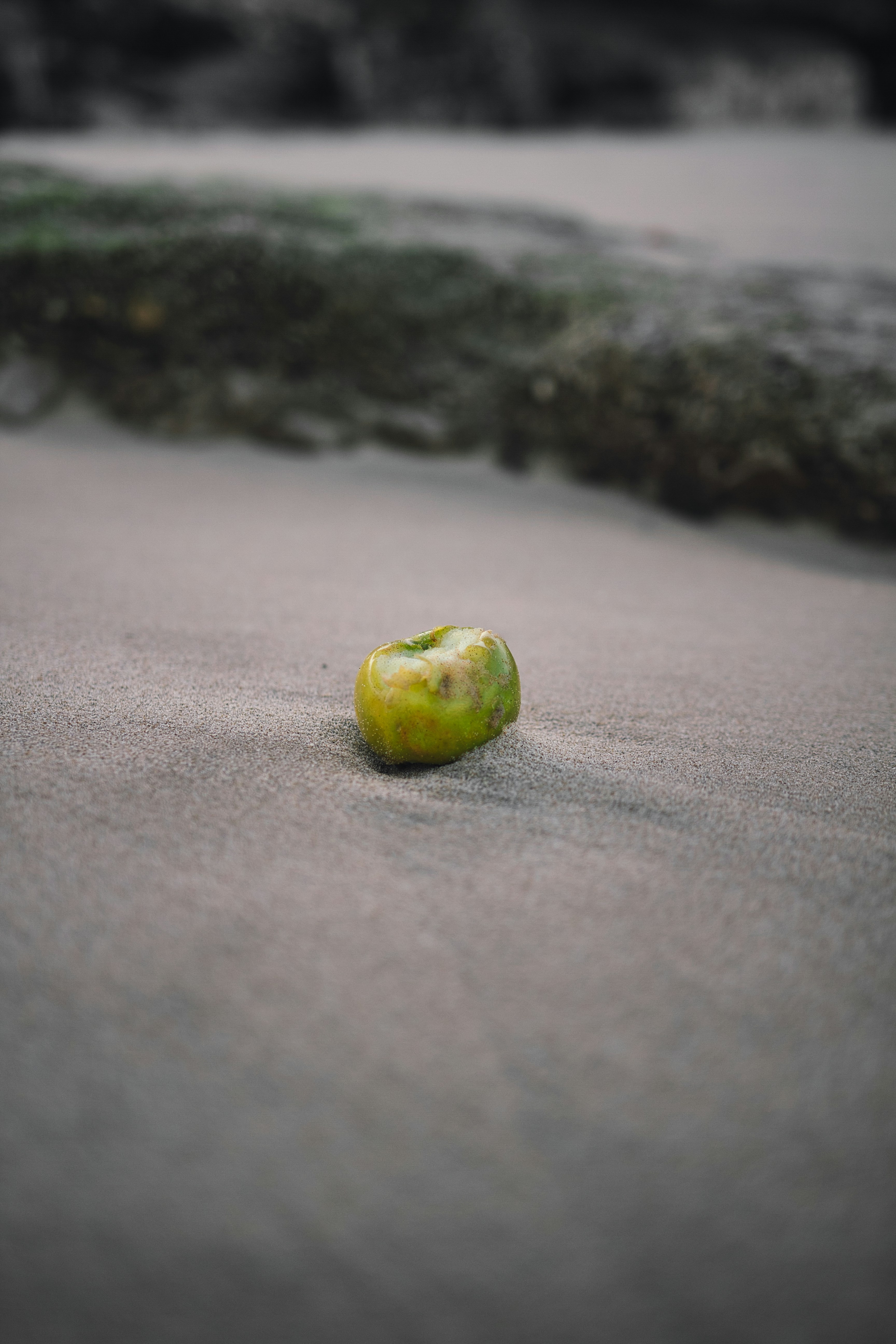 a green apple sitting on top of a sandy beach