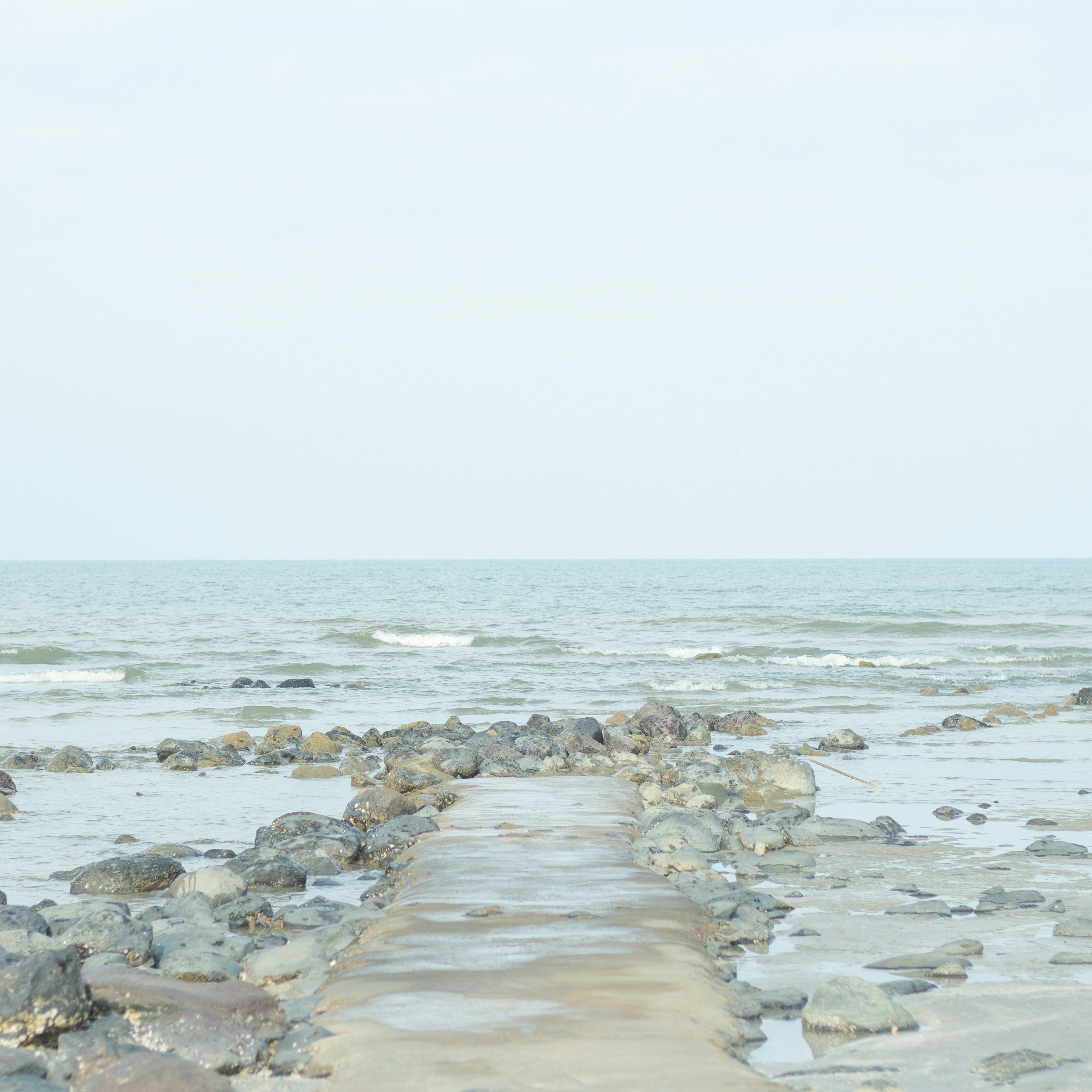 A serene coastal pathway made of stones leading towards the calm sea under a cloudy sky.