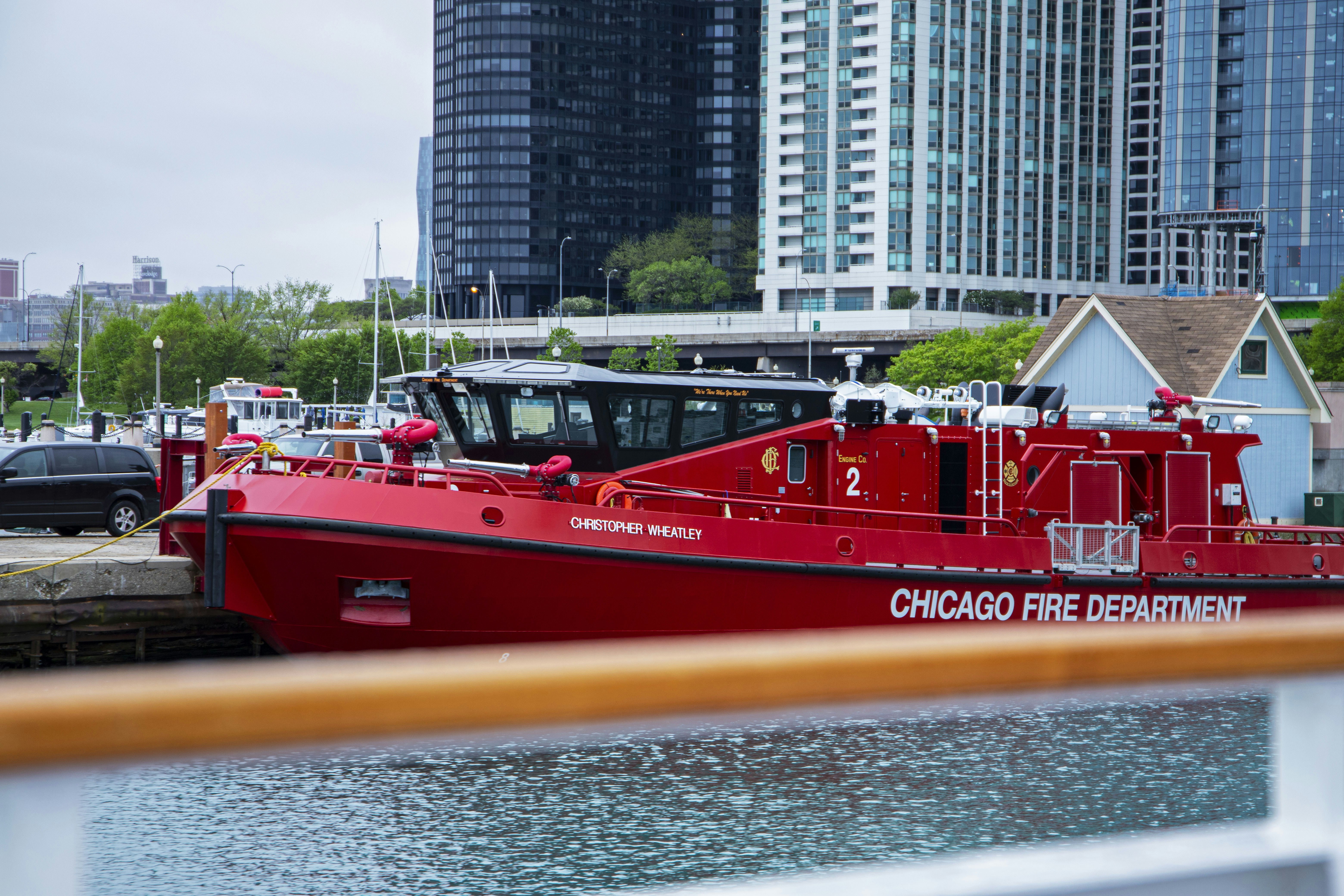 A vibrant red fireboat docked in a marina, showcasing the Chicago Fire Department's vessel against a backdrop of modern architecture.
