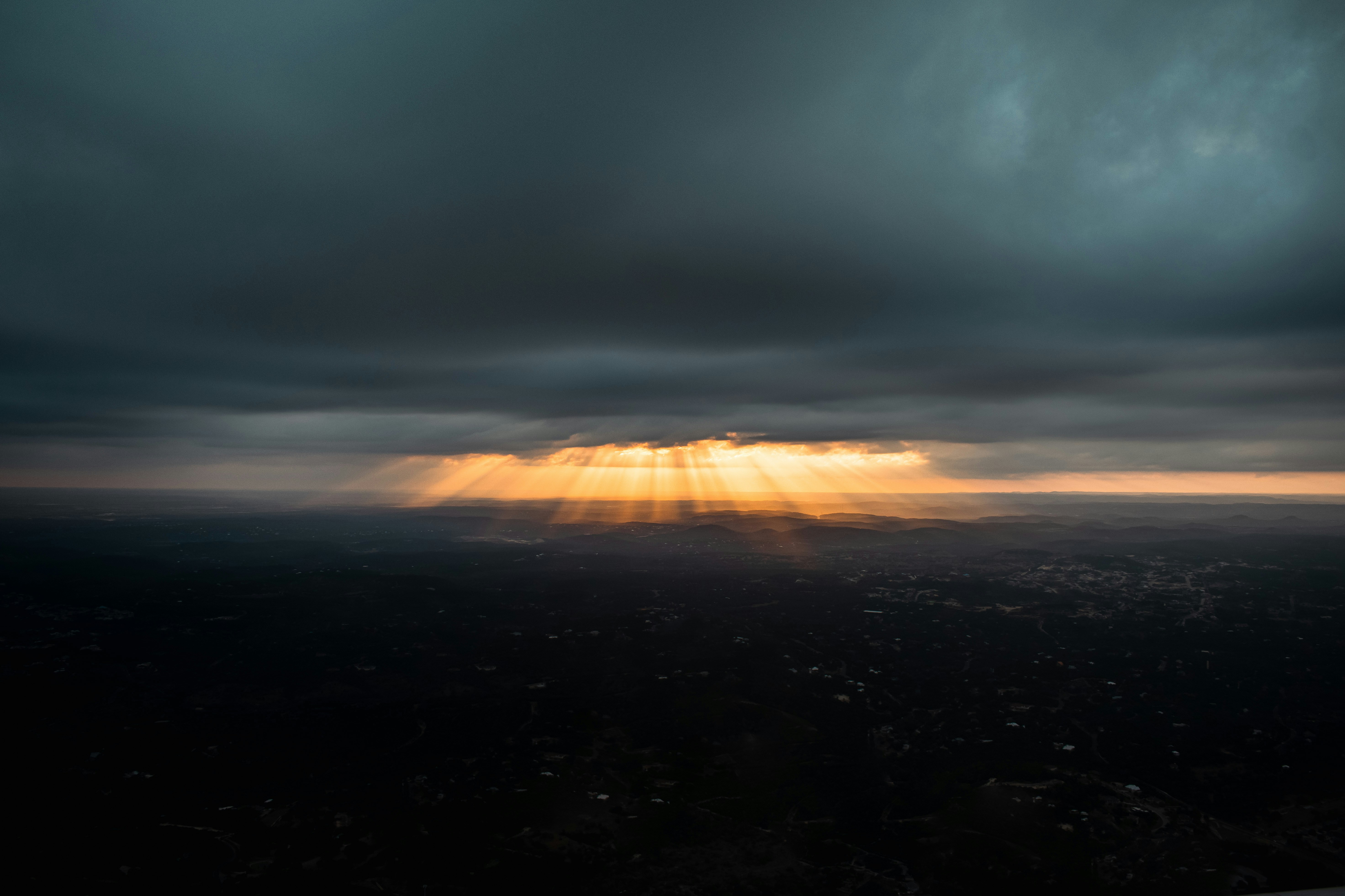 Sunbeams piercing dark clouds over a cityscape at dusk.