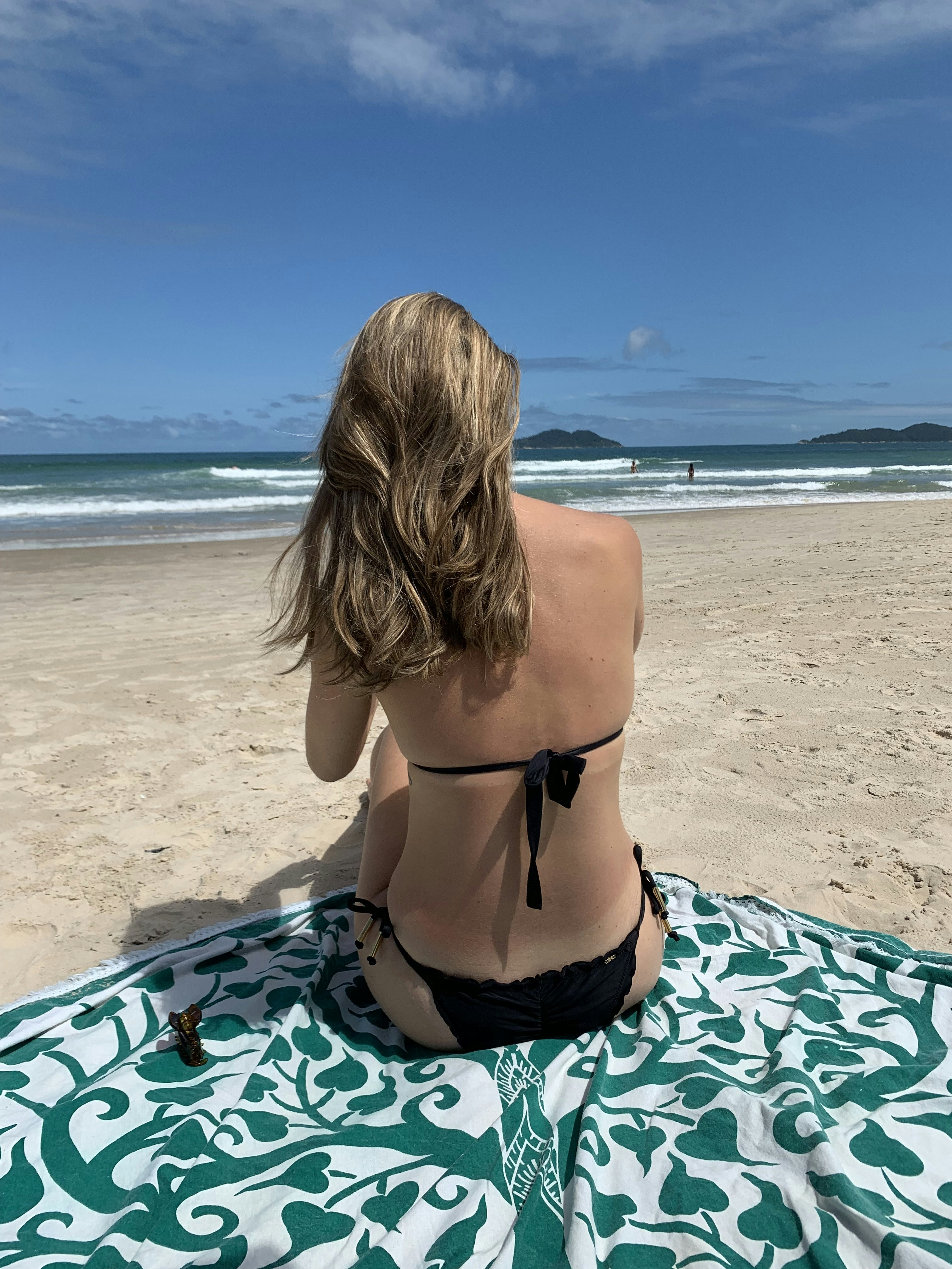 a woman in a bikini sitting on a towel on the beach