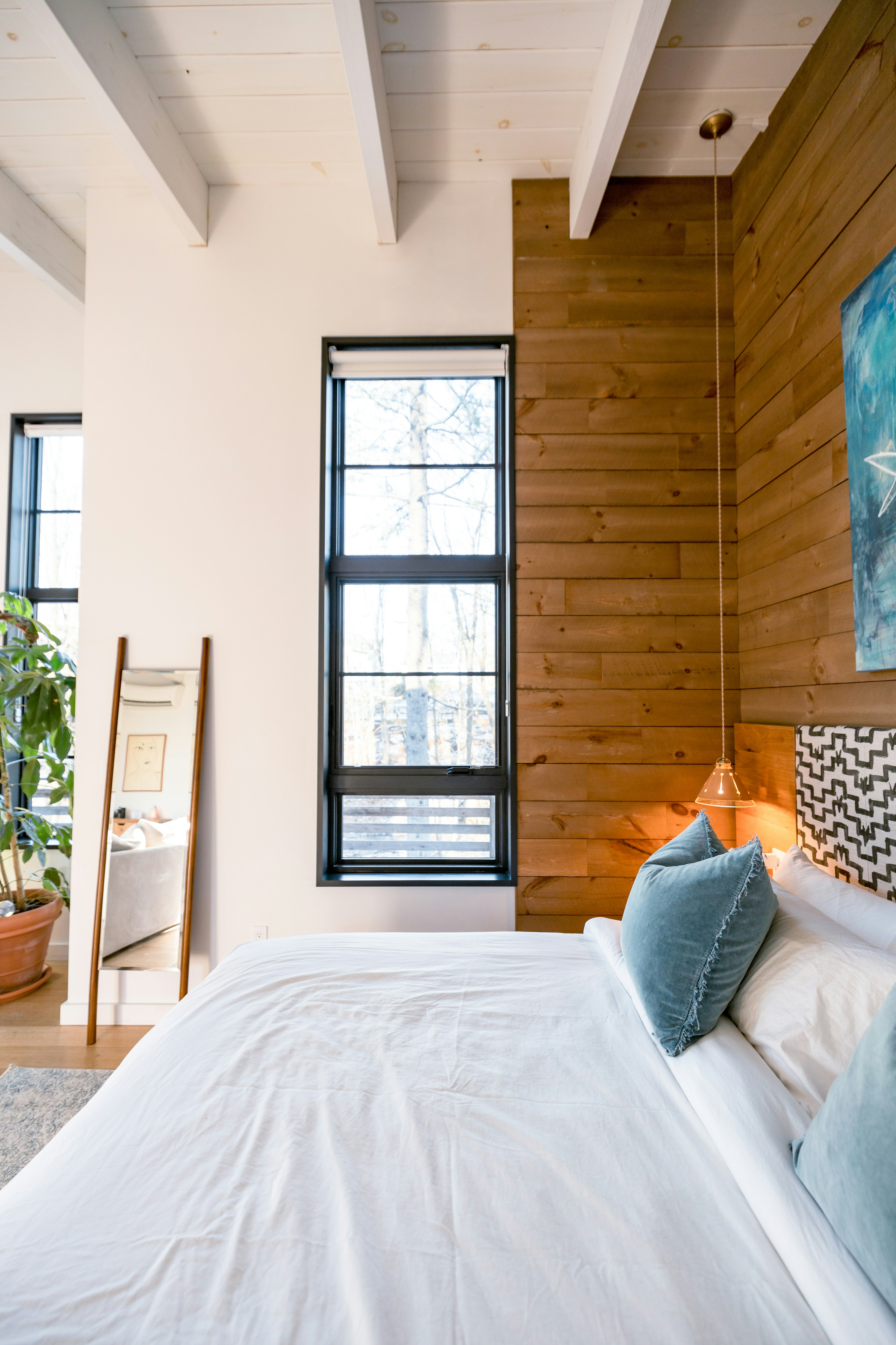 Cozy bedroom featuring a blend of natural wood accents and contemporary decor, with a view of a tranquil outdoor setting through large windows.