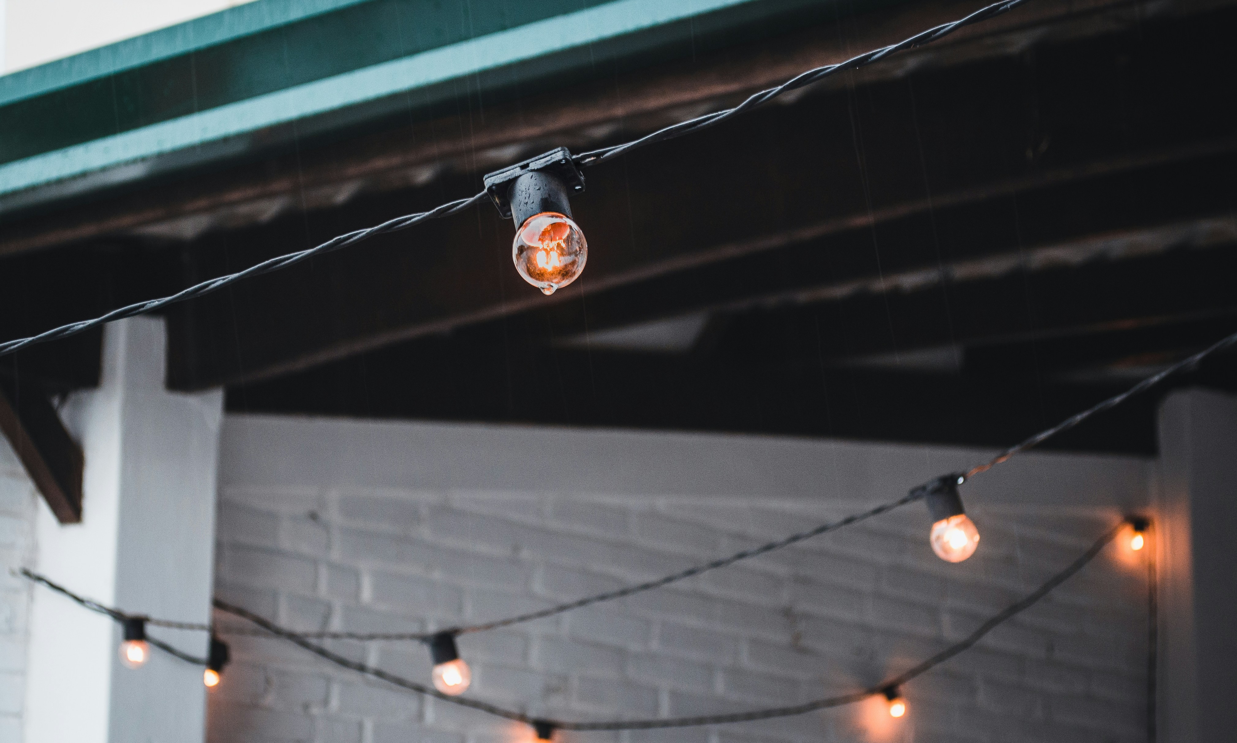 Lone Glow: A single bulb anchors a string of warm lights against a white-brick backdrop.