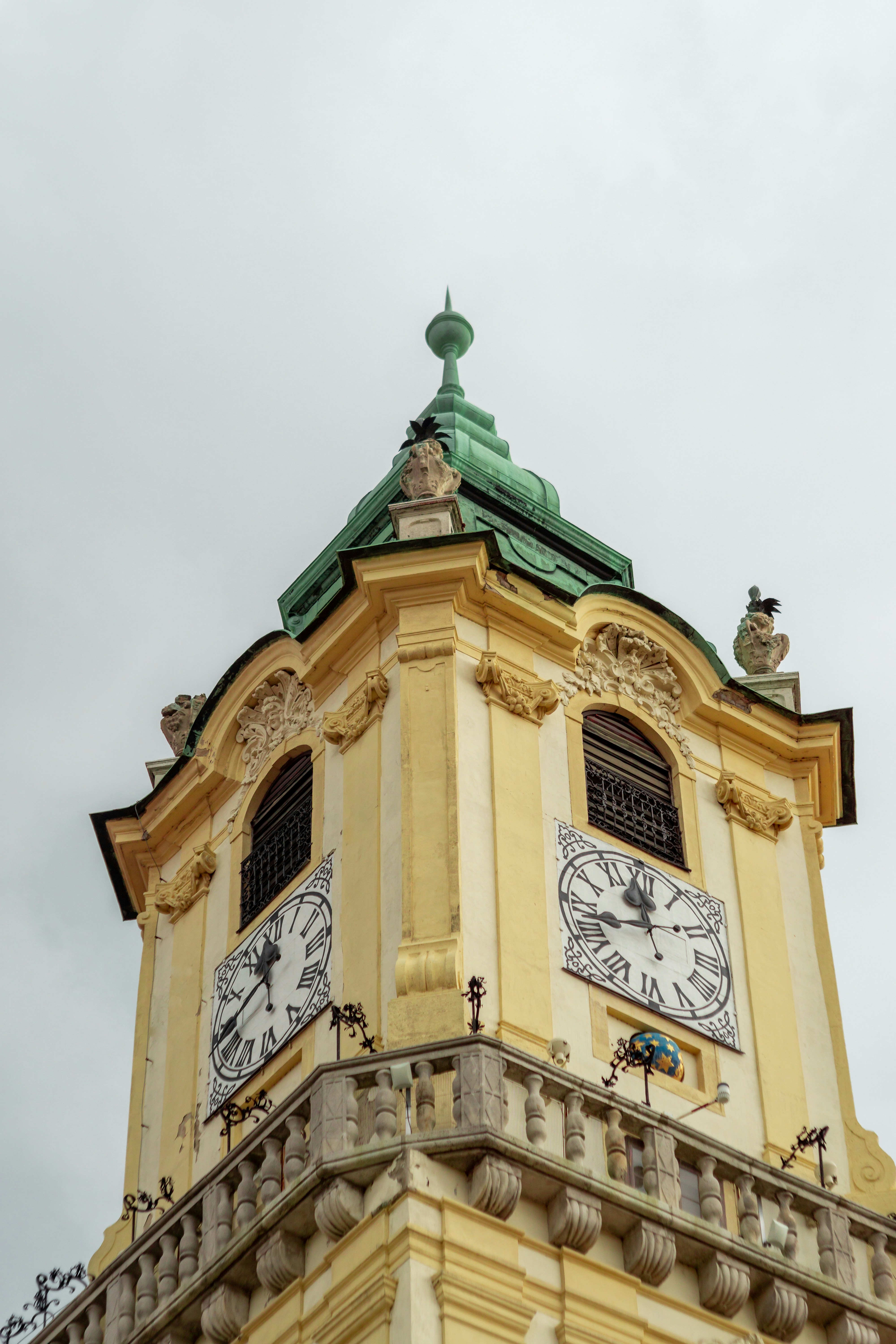 Historic clock tower adorned with intricate architectural details and vibrant green dome against a cloudy sky.