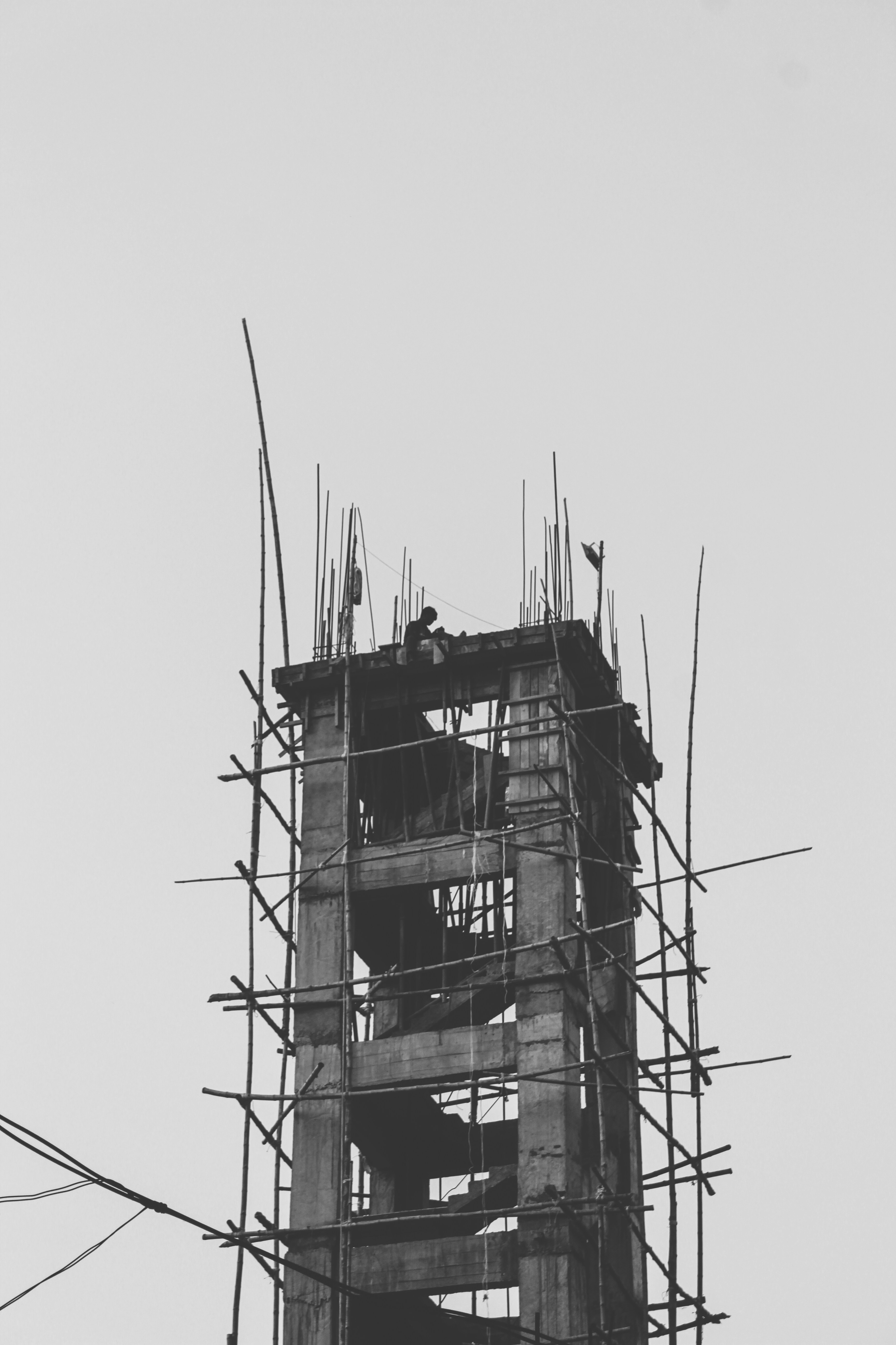 Construction worker navigating scaffolding atop a partially built concrete structure against a pale sky.