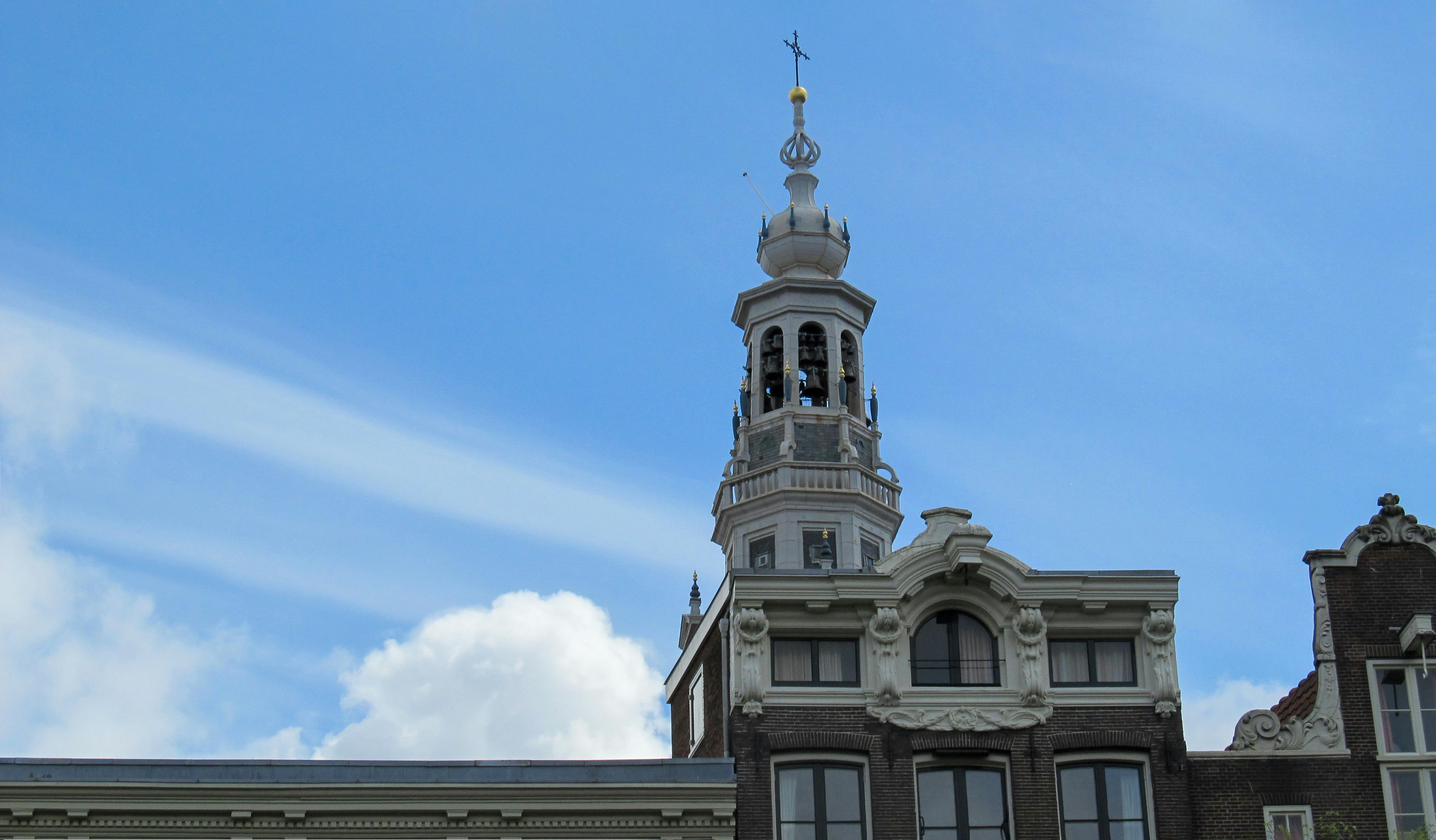 Ornate clock tower rising above a historic building, framed against a bright blue sky with wispy clouds.
