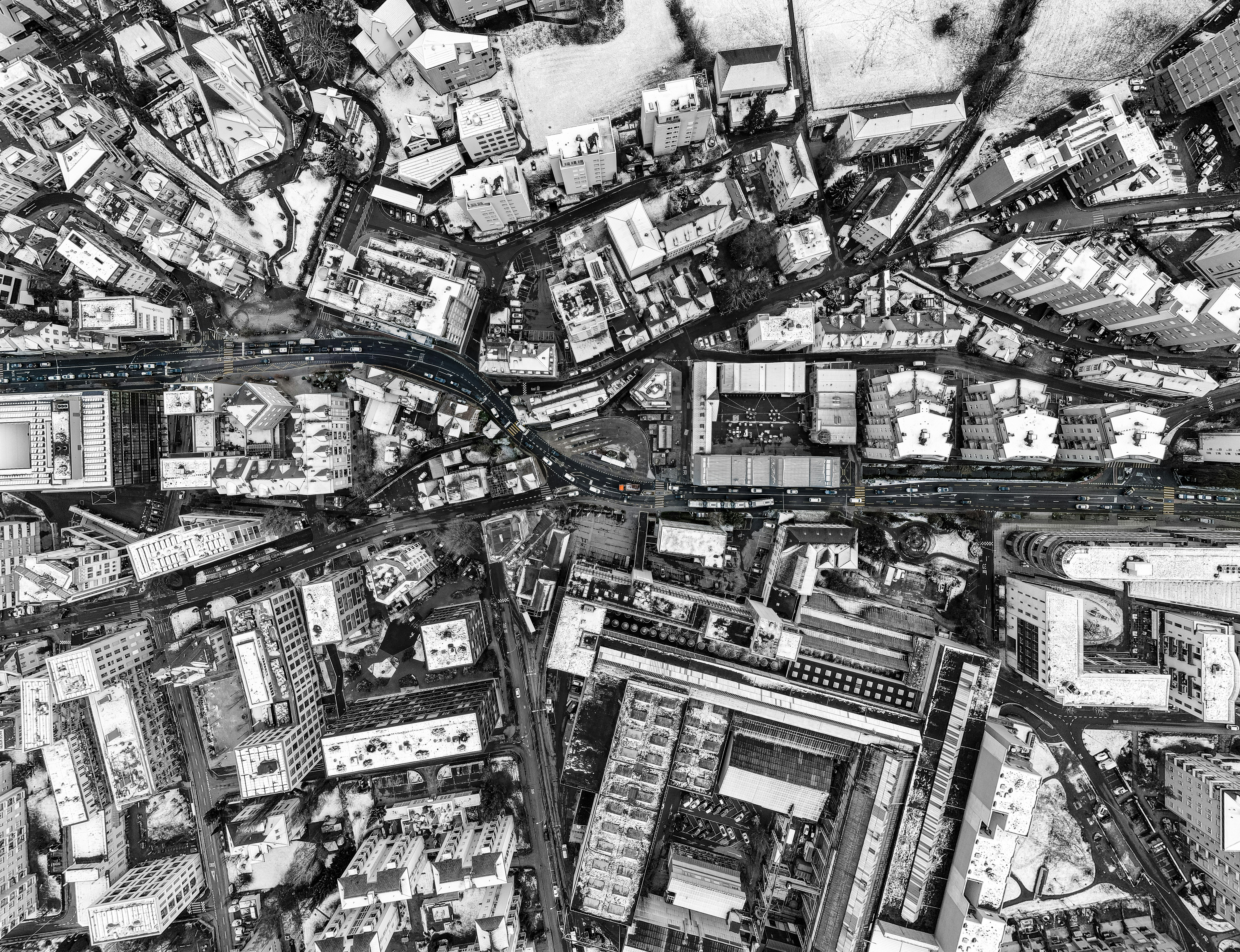 Aerial view of a snow-covered urban landscape, showcasing intricate roadways and buildings blending into a monochromatic pattern.