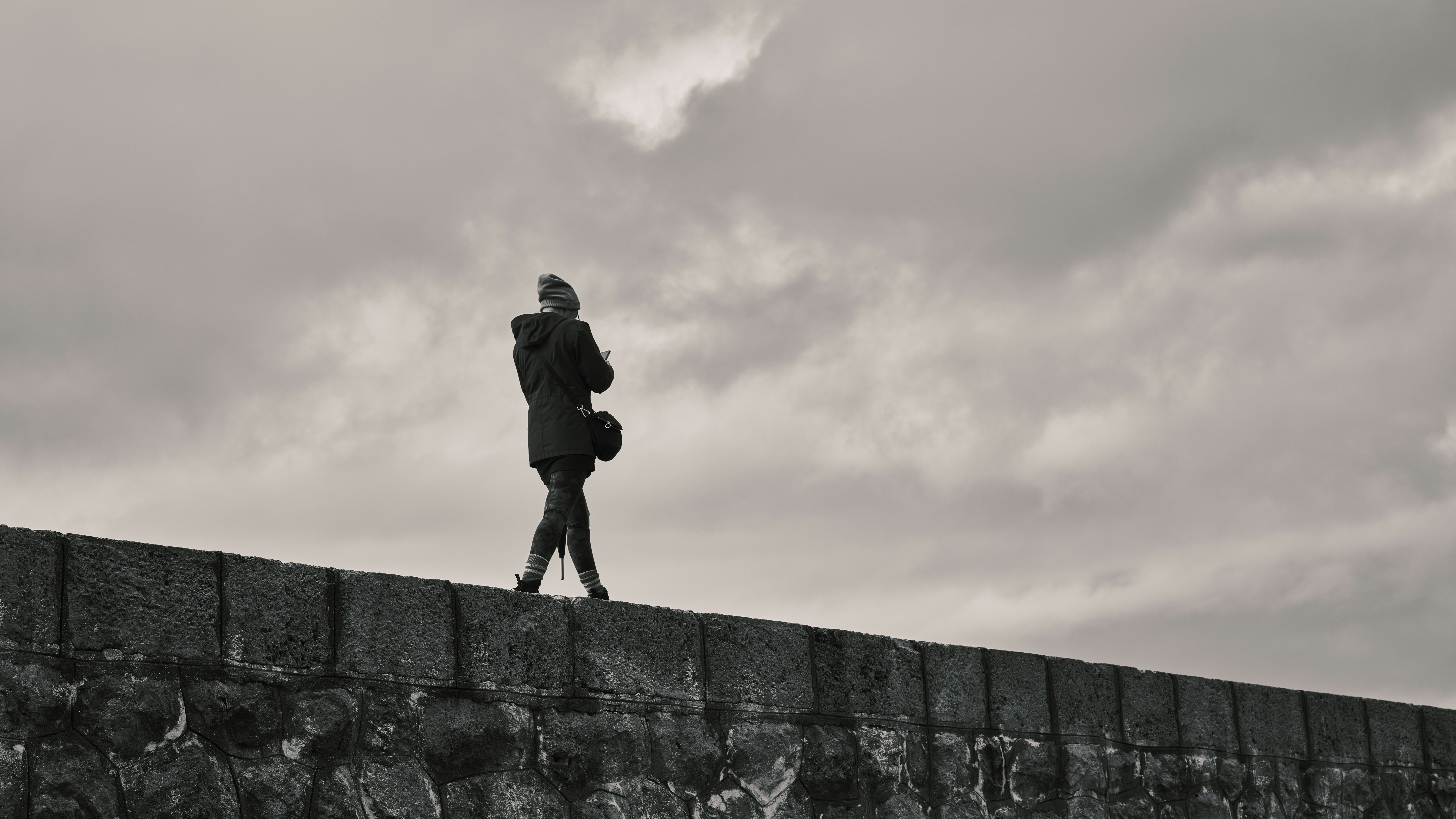 Solitary silhouette pacing a weathered wall beneath a brooding sky