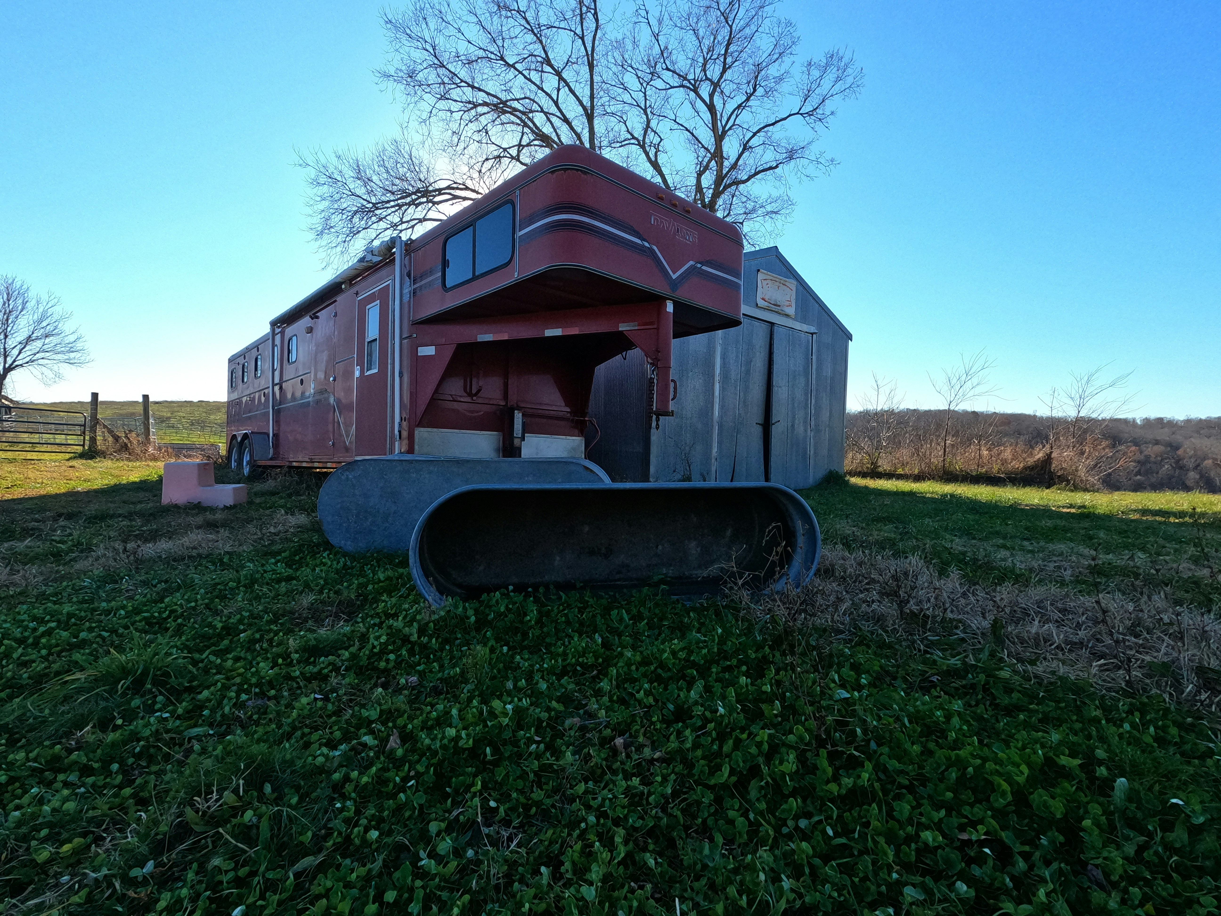 Red horse trailer and wooden shed under clear blue sky in rural landscape.