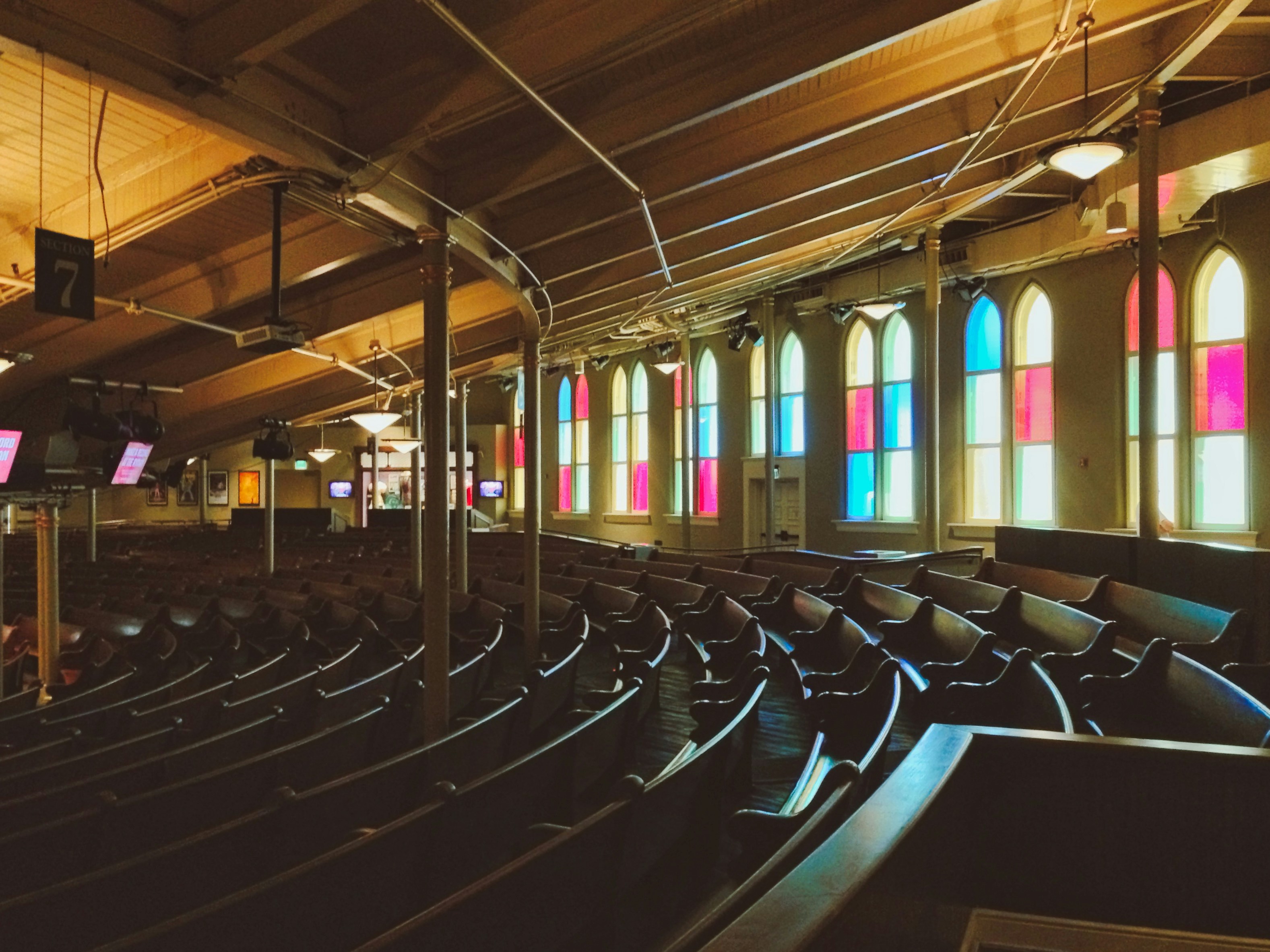 Rows of empty church pews illuminated by colorful stained glass windows.