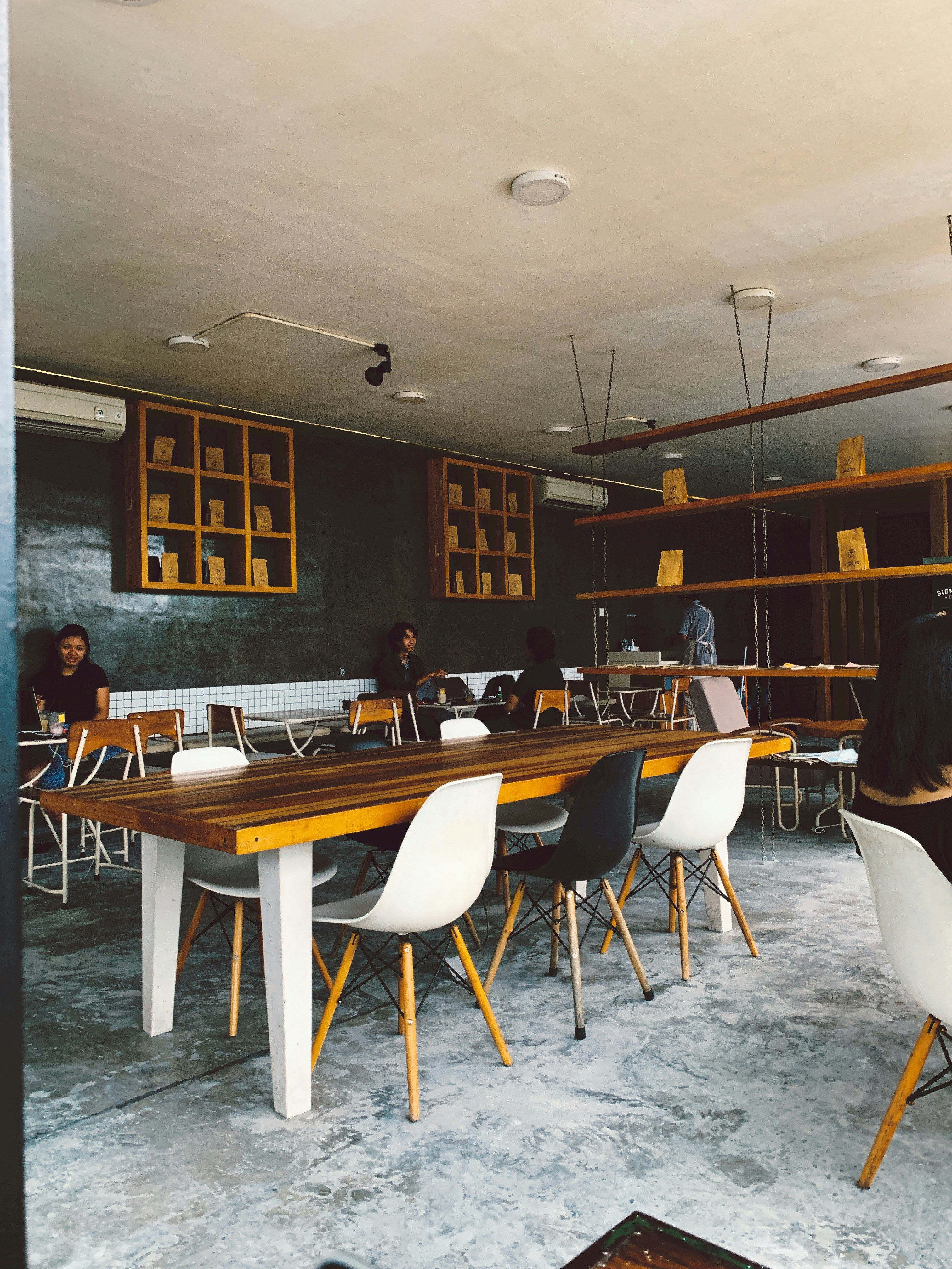 Minimalist café interior featuring wooden tables and white chairs, with patrons engaged in conversation and work.