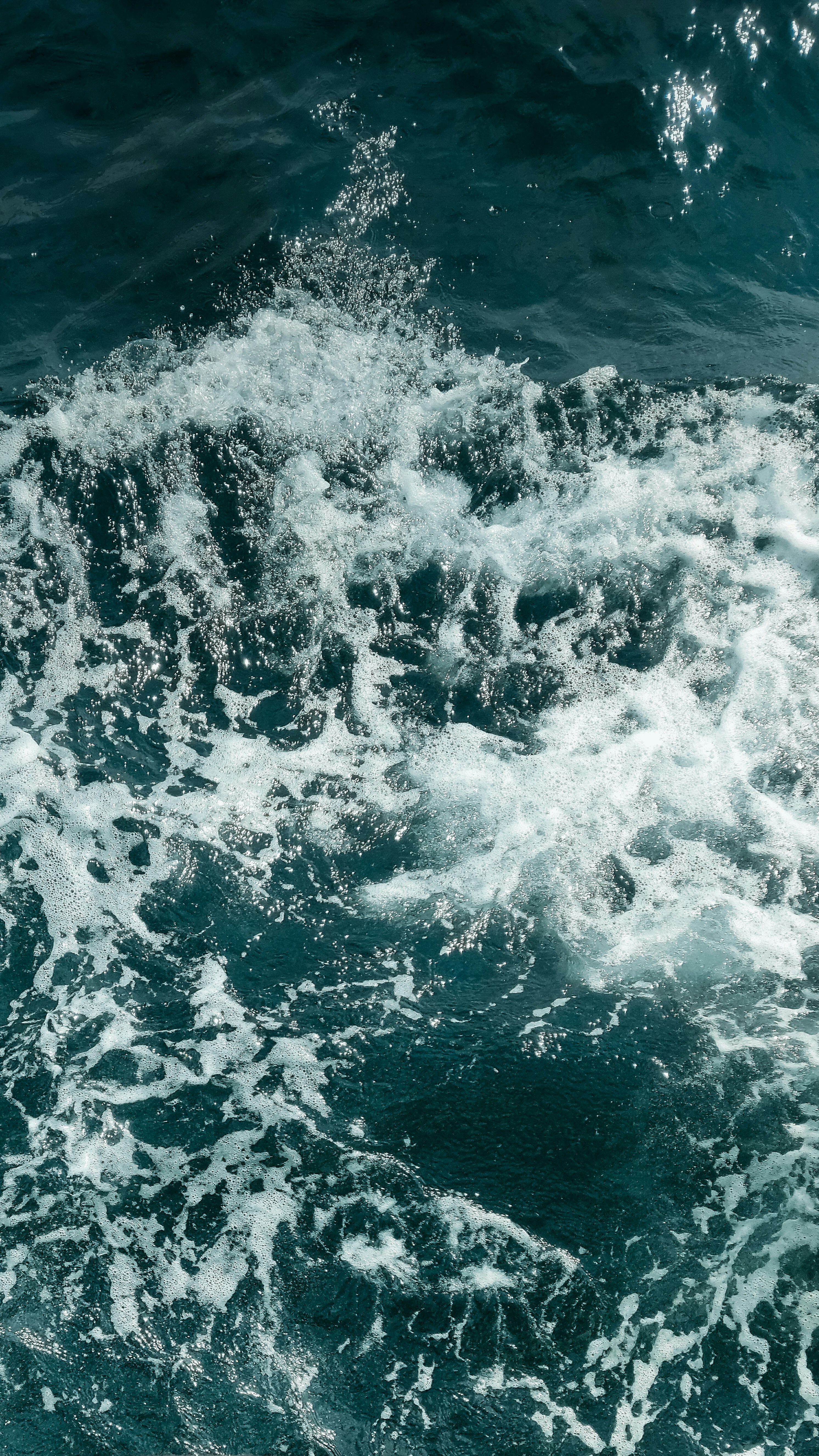 Turbulent ocean waves crashing with foamy white crests against a deep teal backdrop.