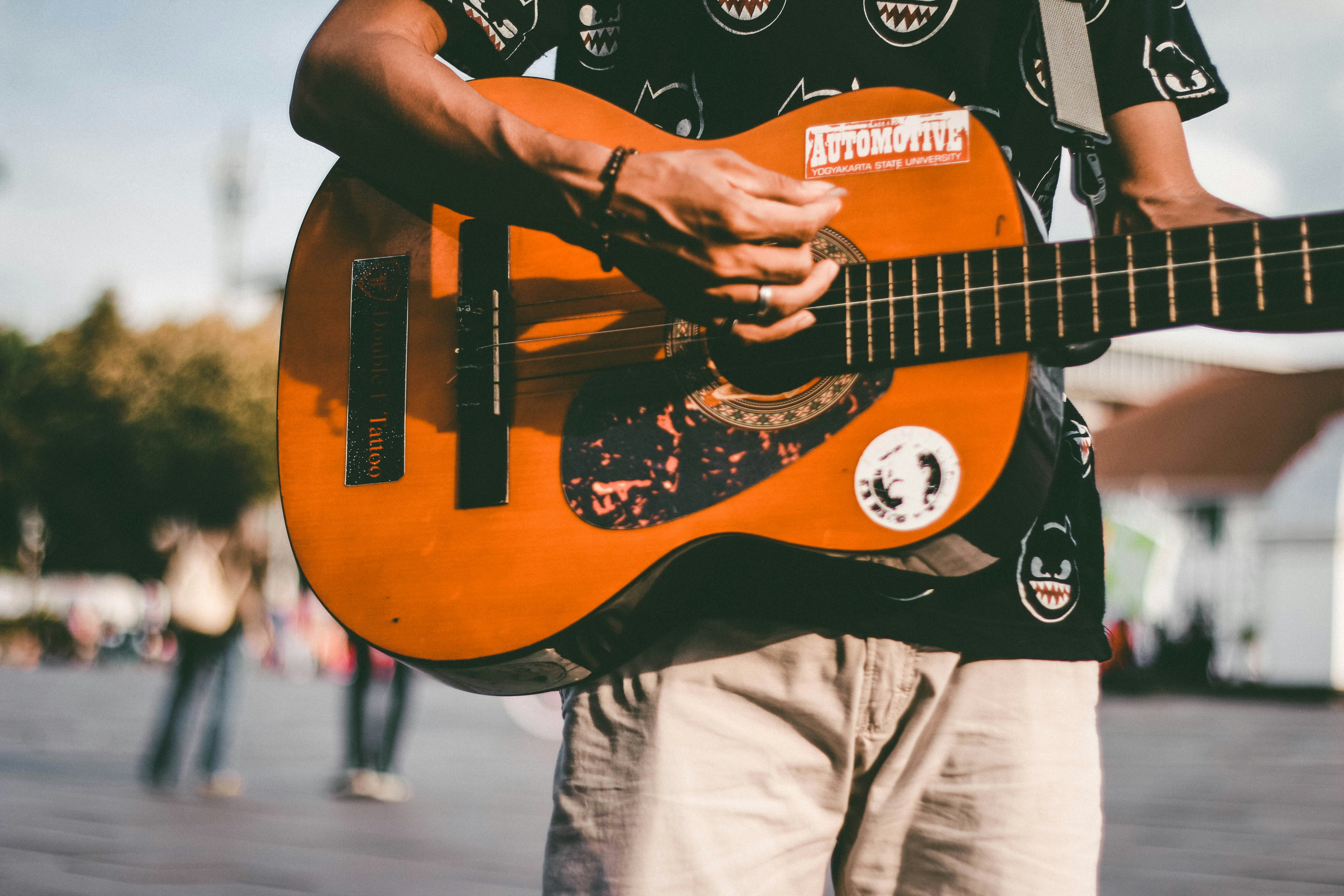 A musician passionately playing an acoustic guitar adorned with stickers, surrounded by a lively urban backdrop.