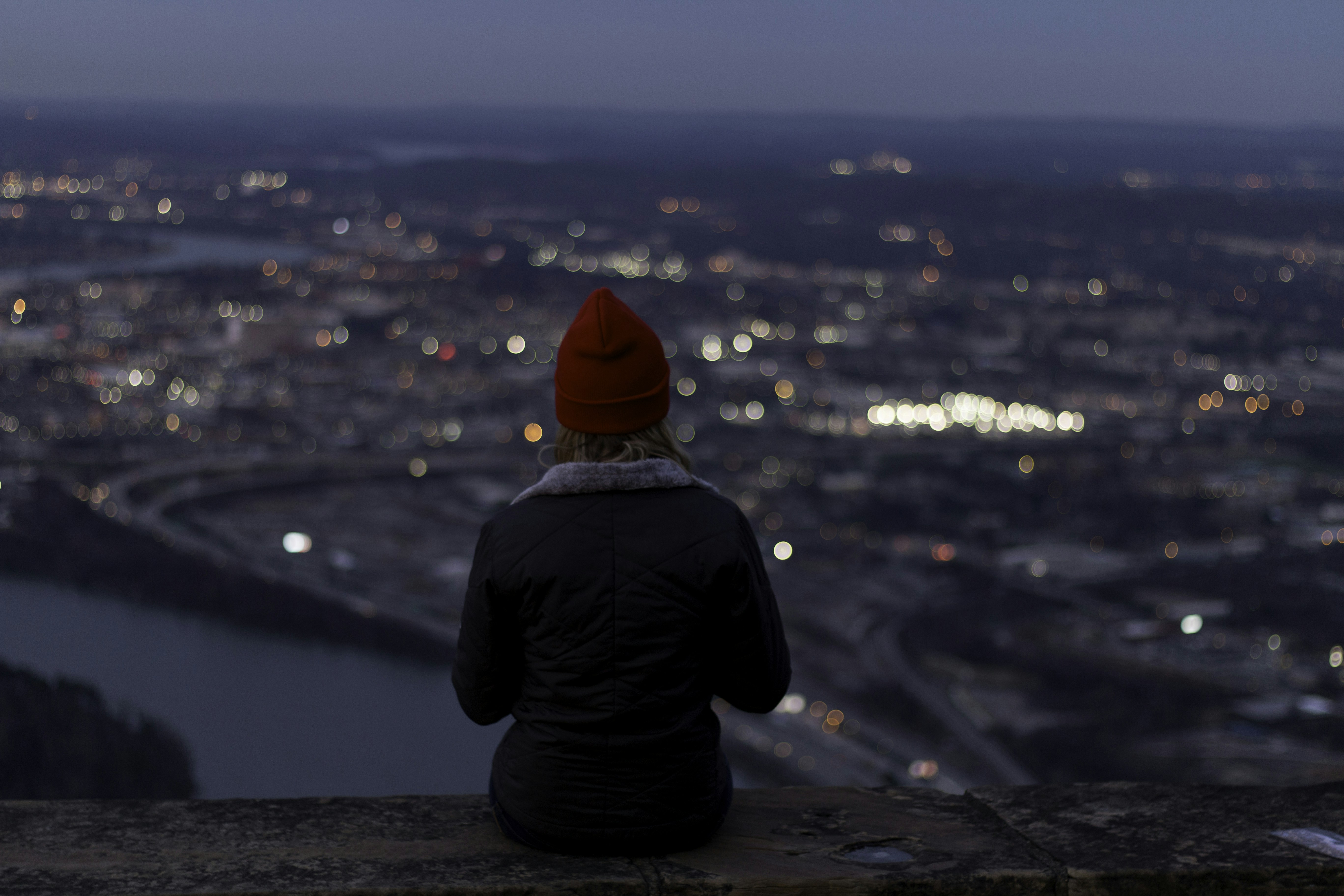A person sitting on a ledge overlooking a city at night photo – Free ...