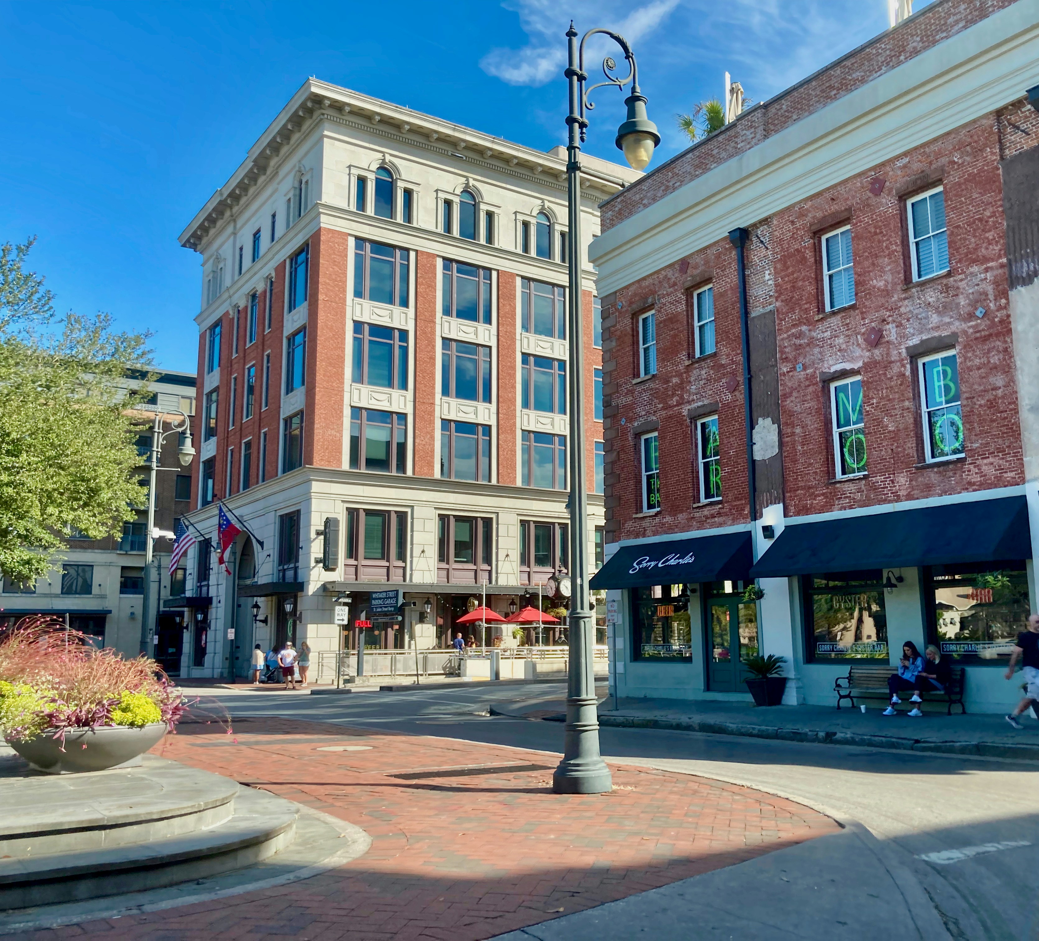 Charming street view showcasing a blend of historic and modern buildings, with outdoor seating and decorative planters. Flags and signage add character to the vibrant urban scene.