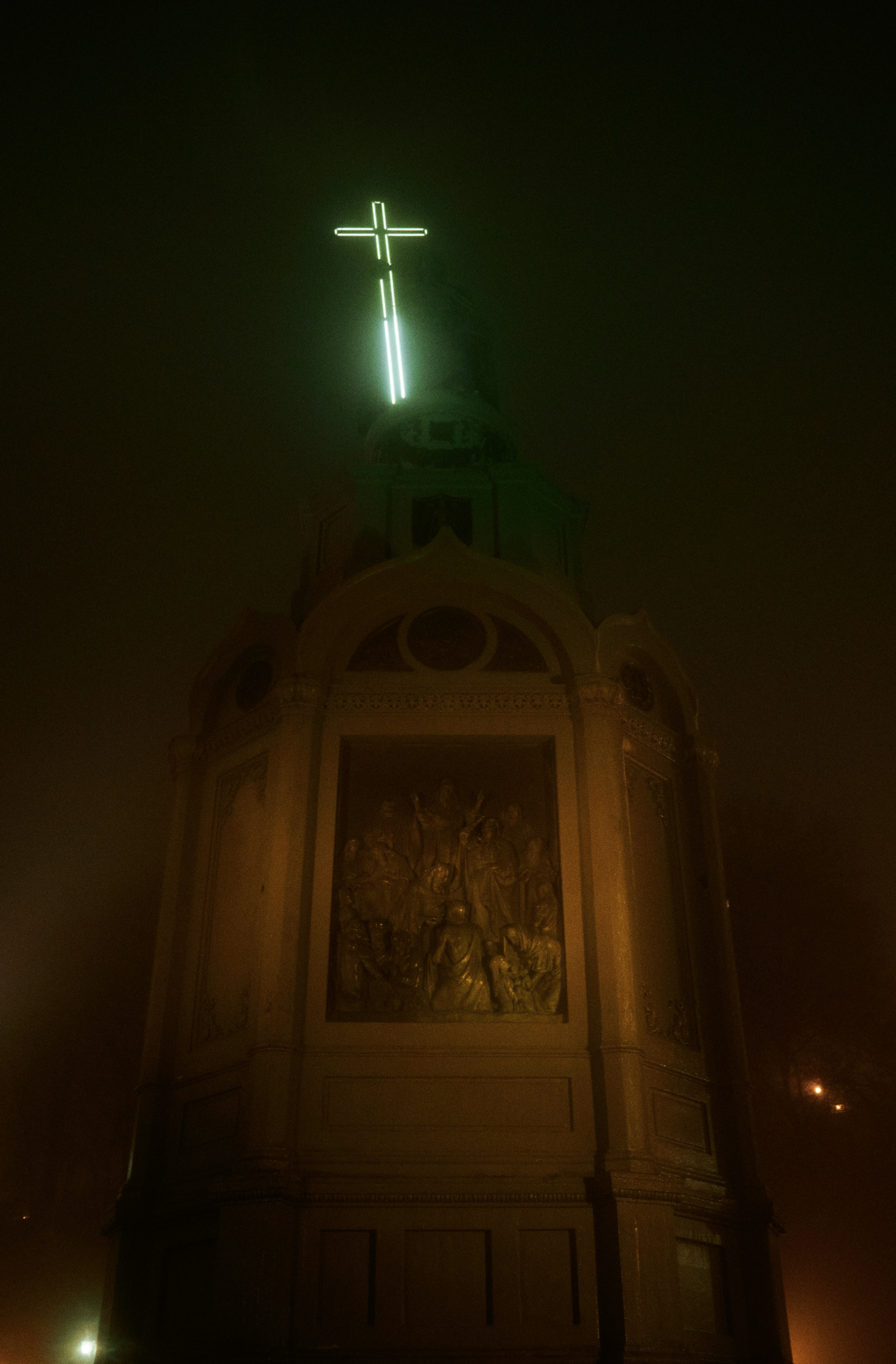 Glowing cross atop a misty monument in nocturnal glow