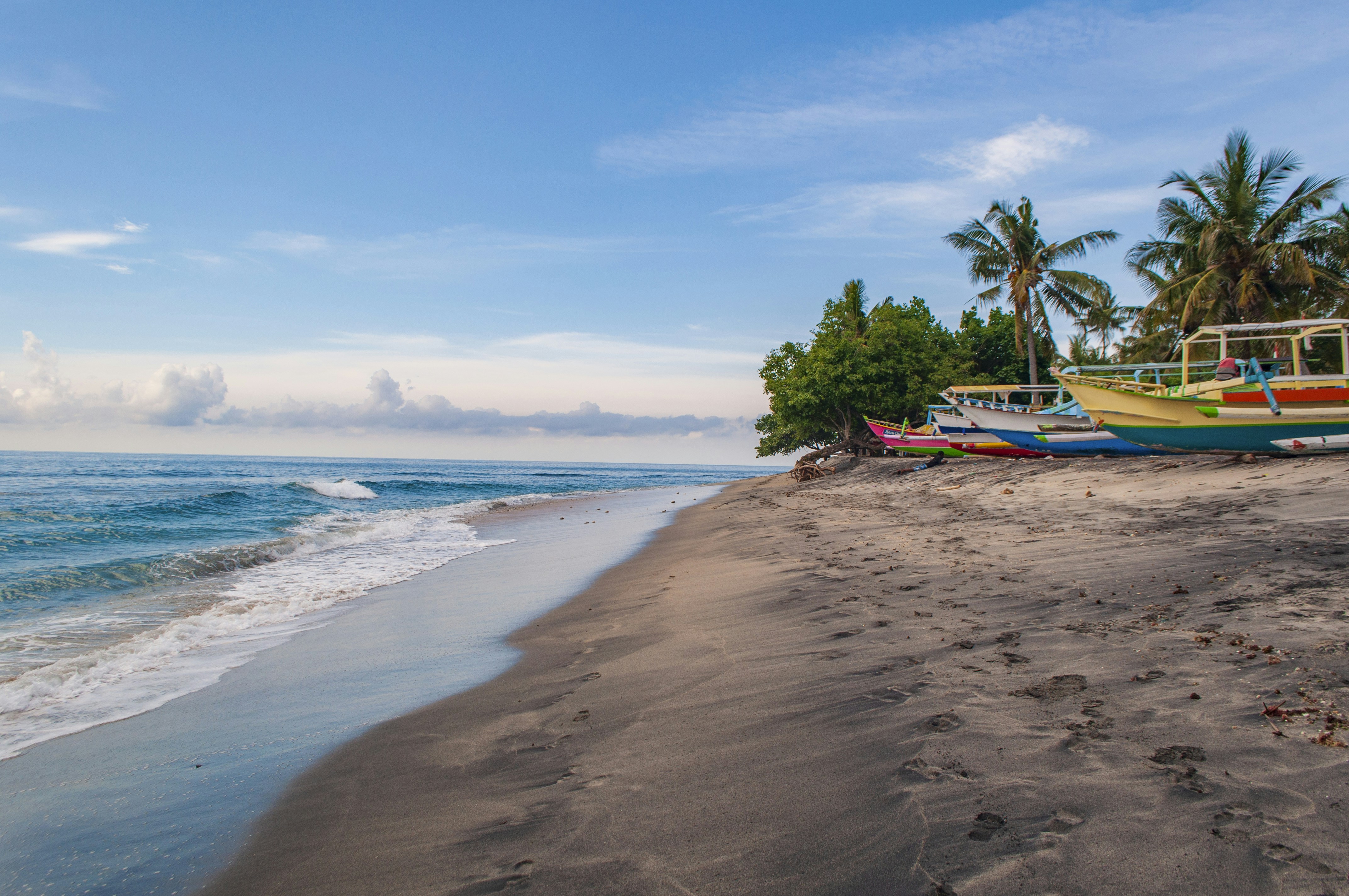 Colorful fishing boats resting on a tranquil beach with gentle waves lapping at the shore under a clear sky.