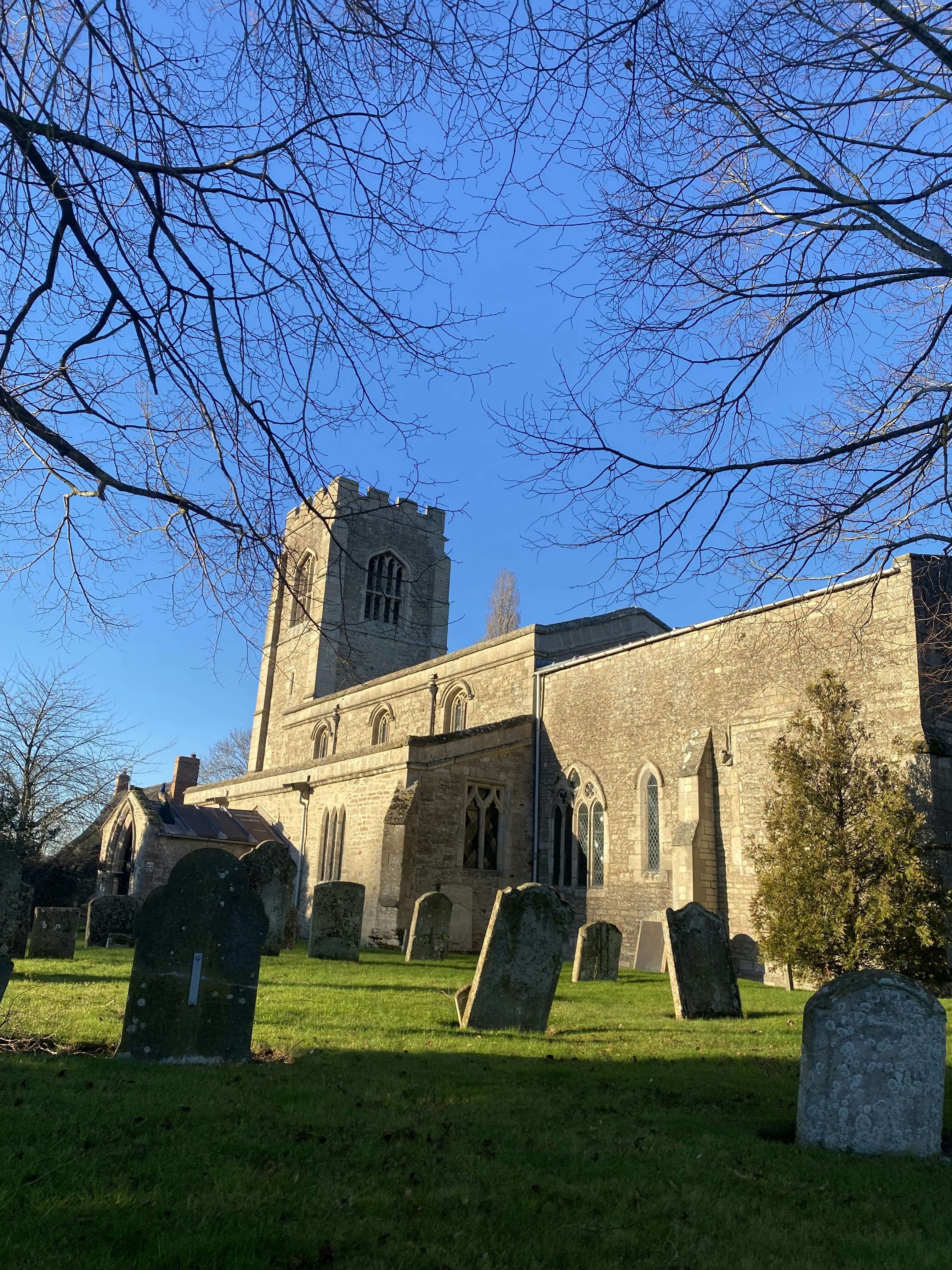 Historic church with a tall tower surrounded by gravestones under a clear blue sky. The scene captures a serene moment in a tranquil setting.