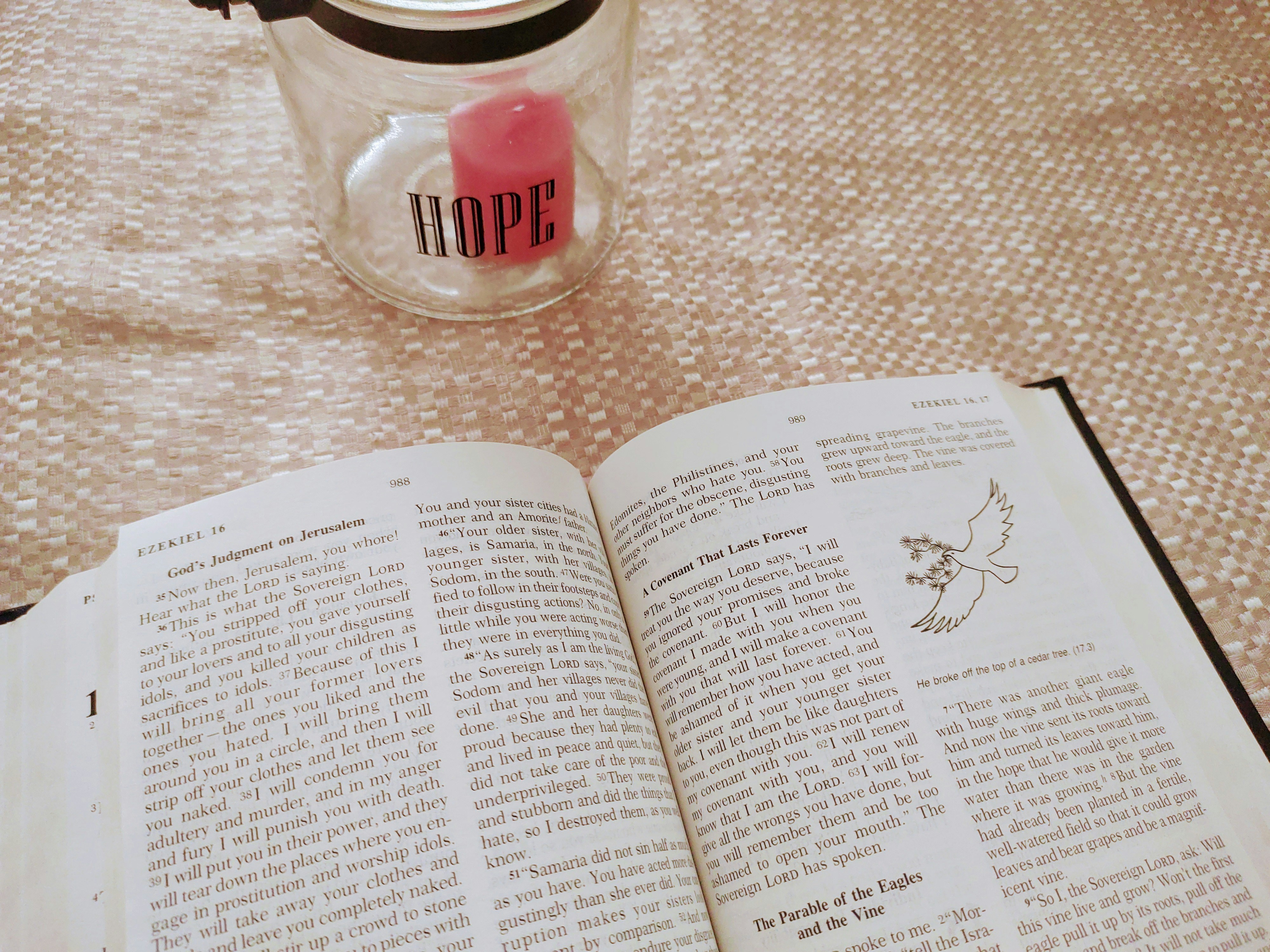 Open book on a textured surface with a small pink candle labeled 'HOPE' in the background, conveying a calm reading scene.