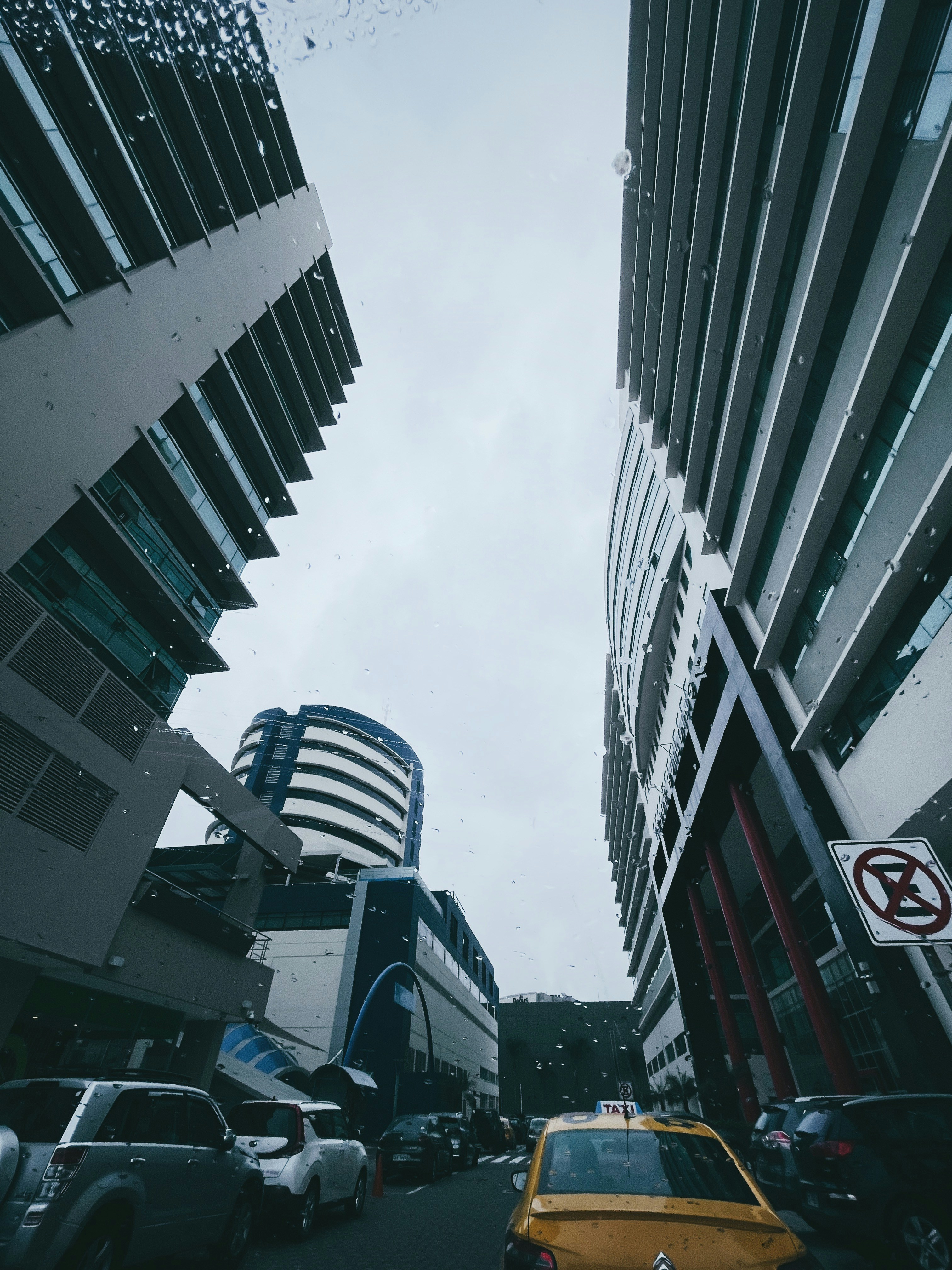 Yellow taxi navigating a rainy street flanked by towering modern buildings.