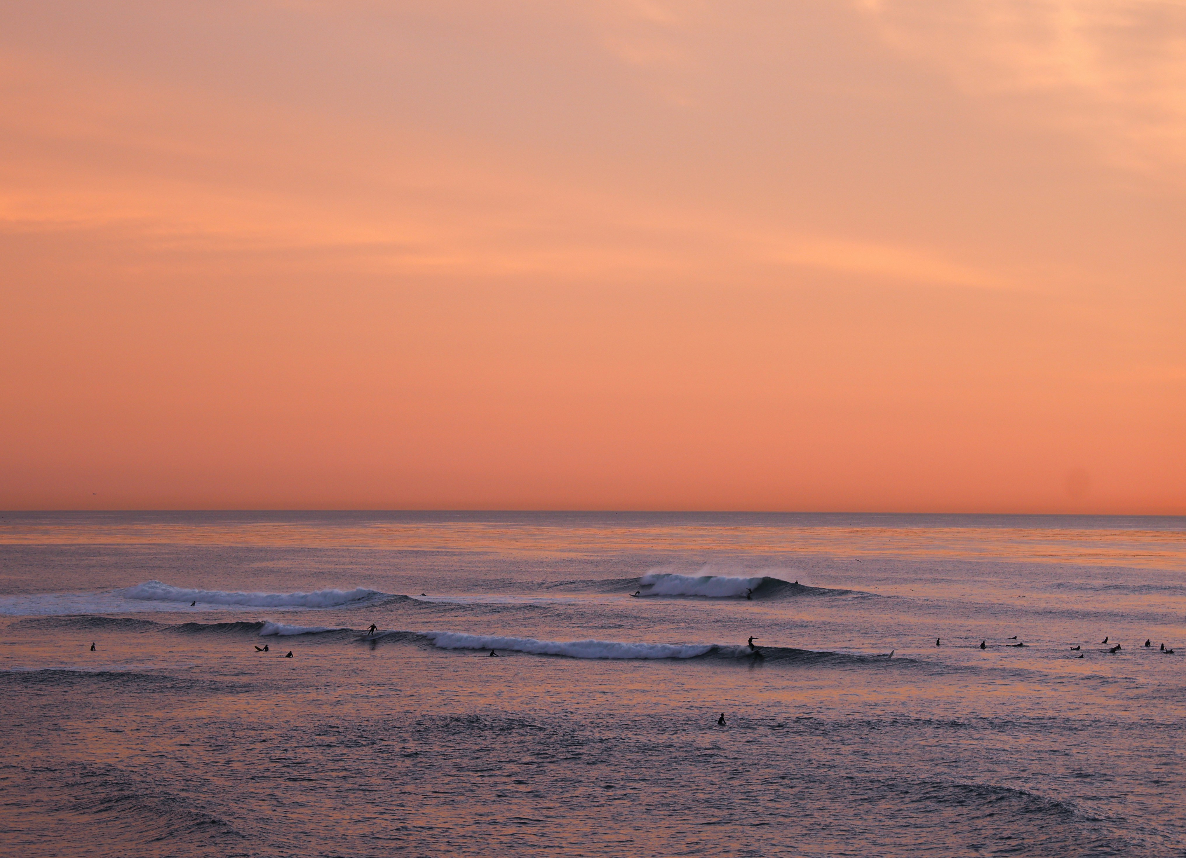 Foto zum Thema Eine Gruppe von Surfern im Ozean bei Sonnenuntergang ...