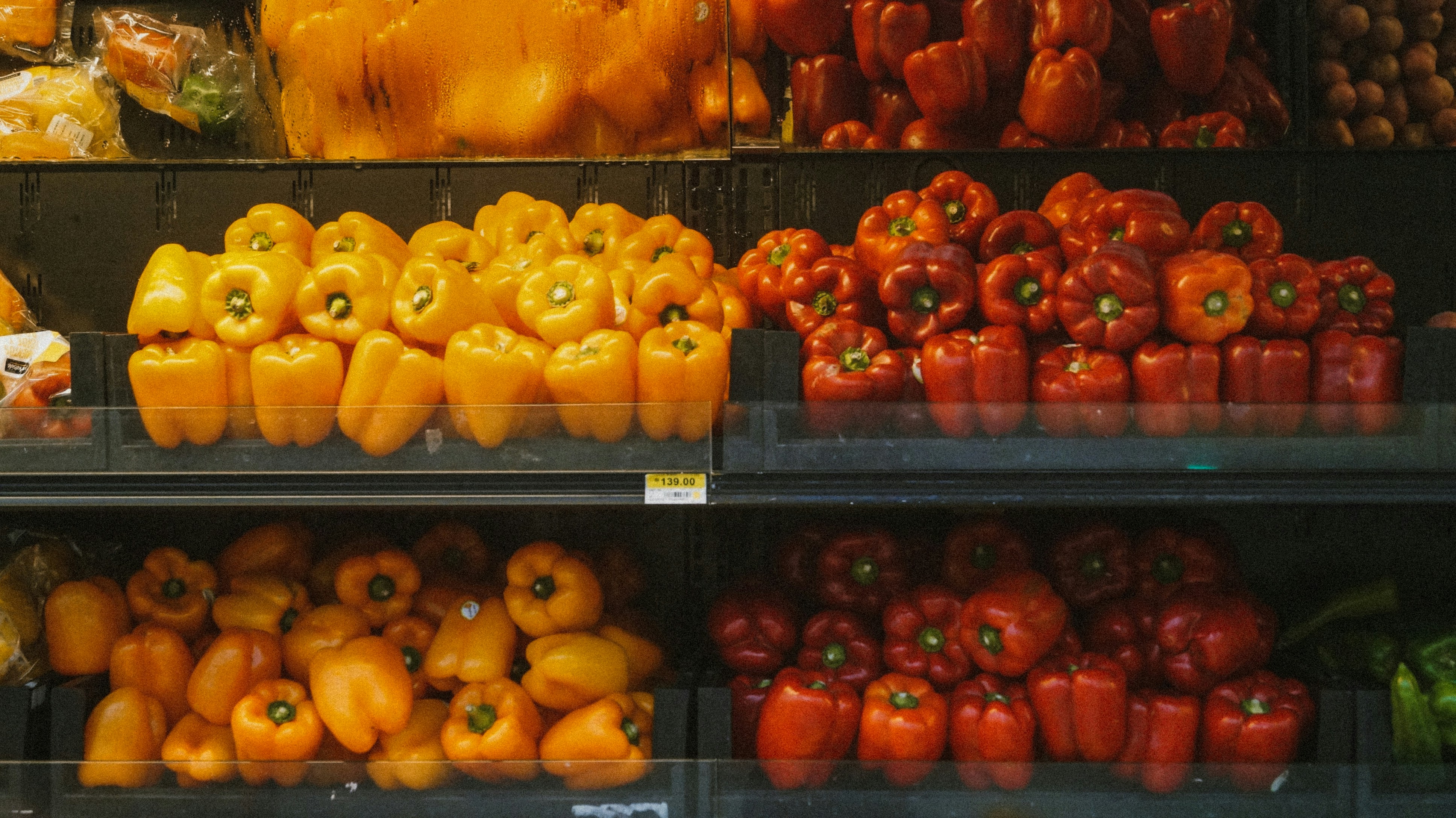 Colorful display of yellow and red bell peppers arranged on shelves in a grocery store, showcasing their freshness and variety.