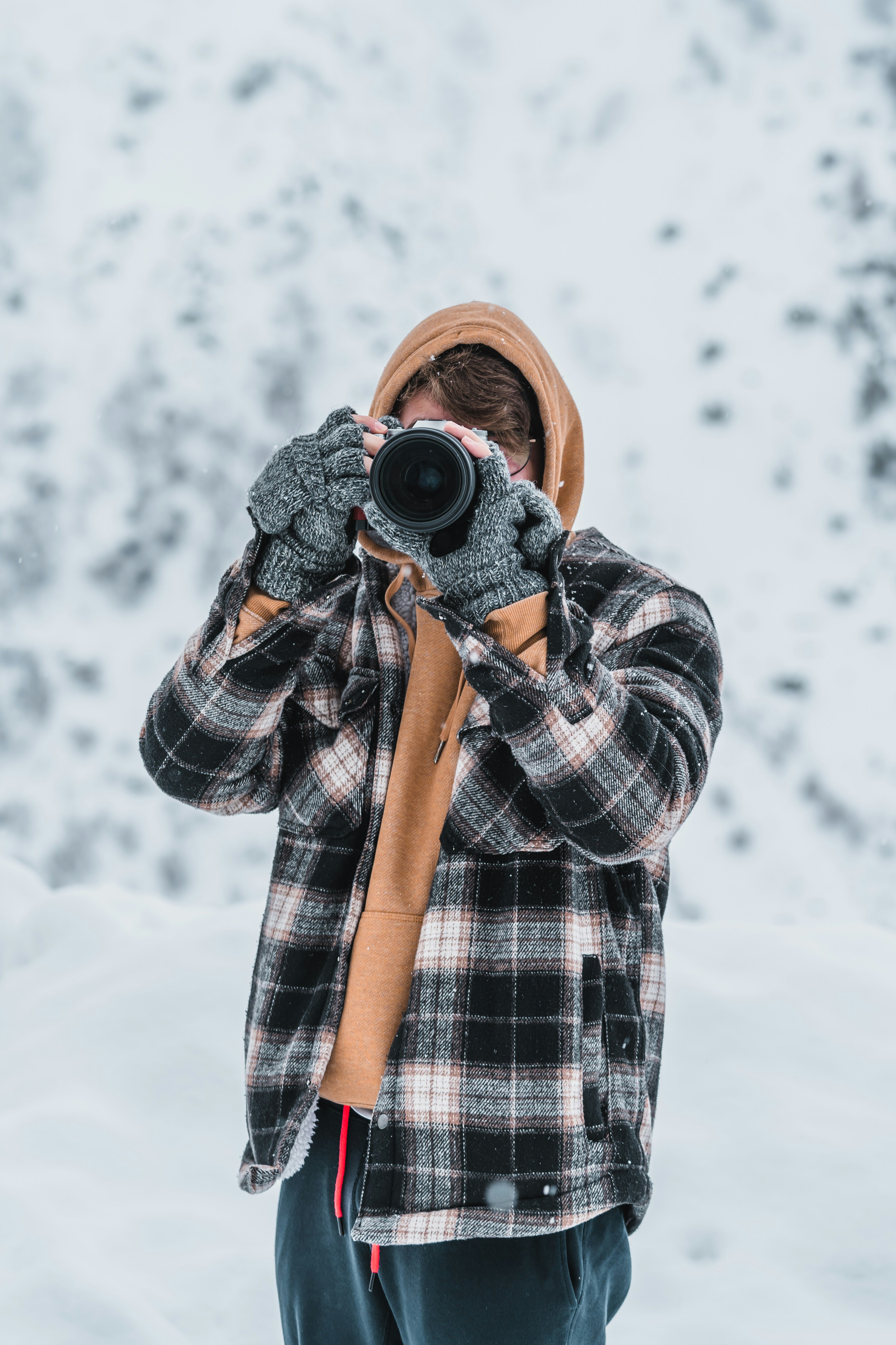 A photographer dressed in winter attire aims their camera amidst a snowy landscape, capturing the essence of the cold season.