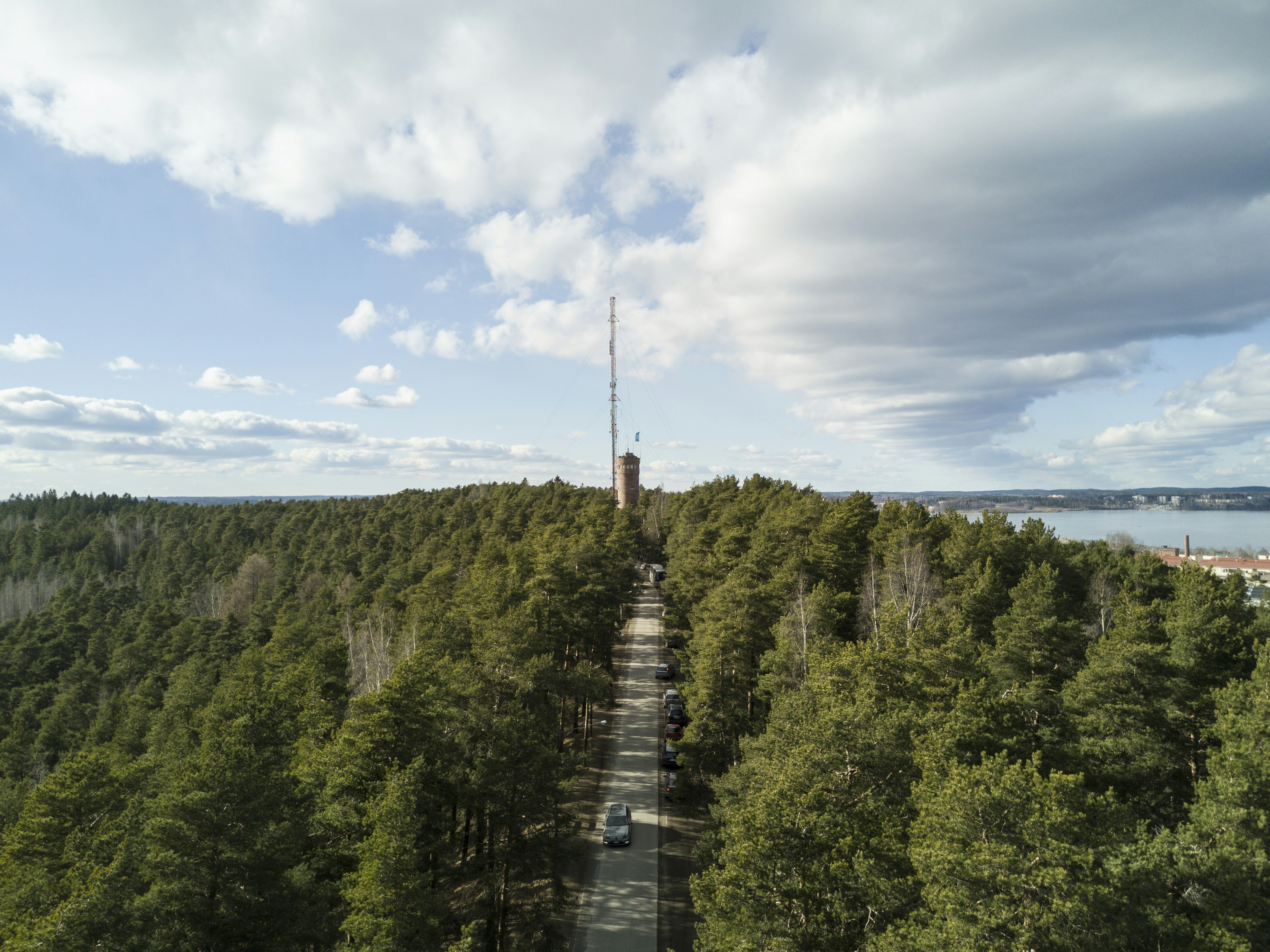 A solitary tower rises above a dense forest under a partly cloudy sky.
