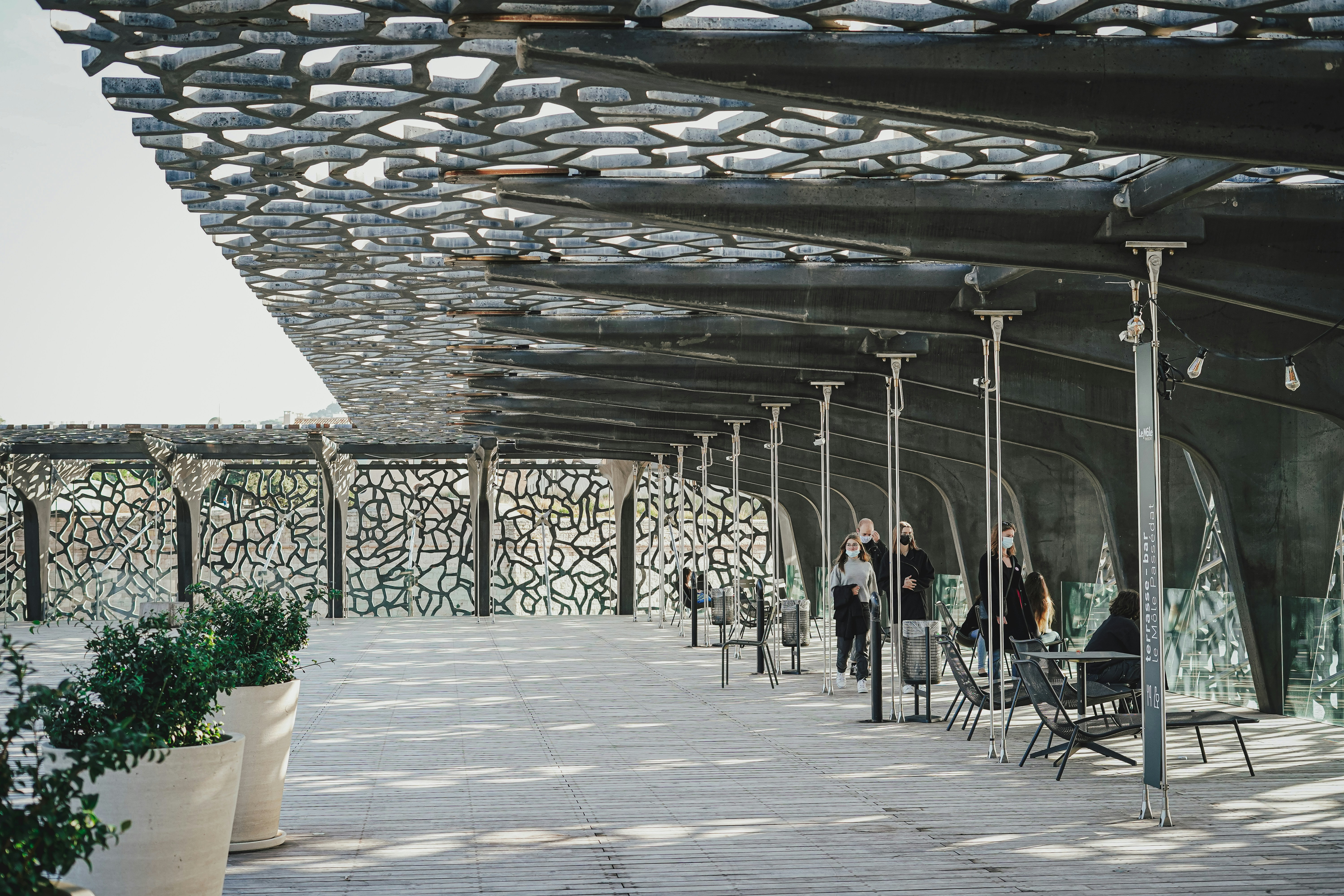 Terrace in Light: People on a Glass-Walled Patio Beneath a Geometric Canopy