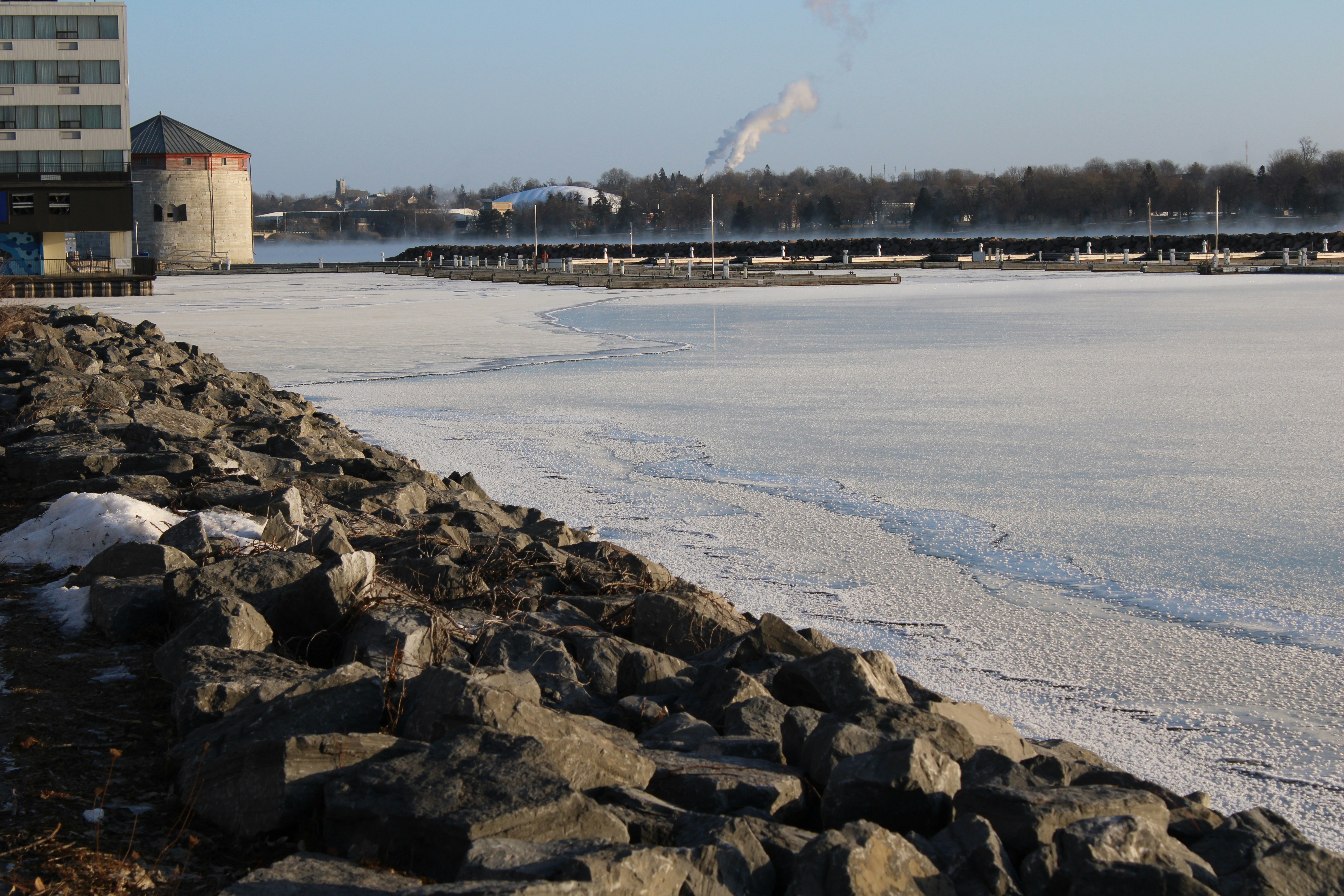 Rocky shoreline meets a partially frozen body of water under a clear blue sky.