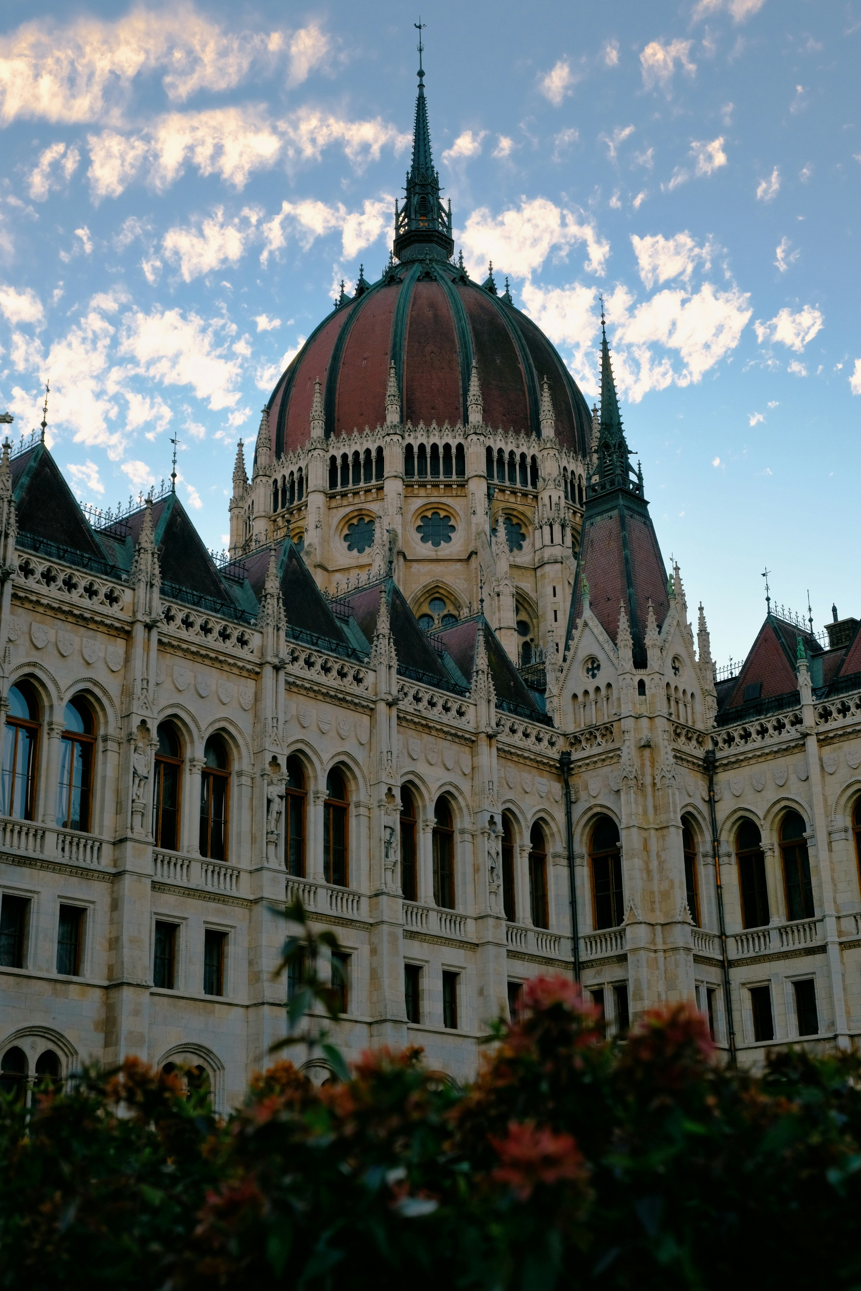 The ornate dome of a historic building rises against a backdrop of wispy clouds, framed by intricate architectural details and lush foliage.
