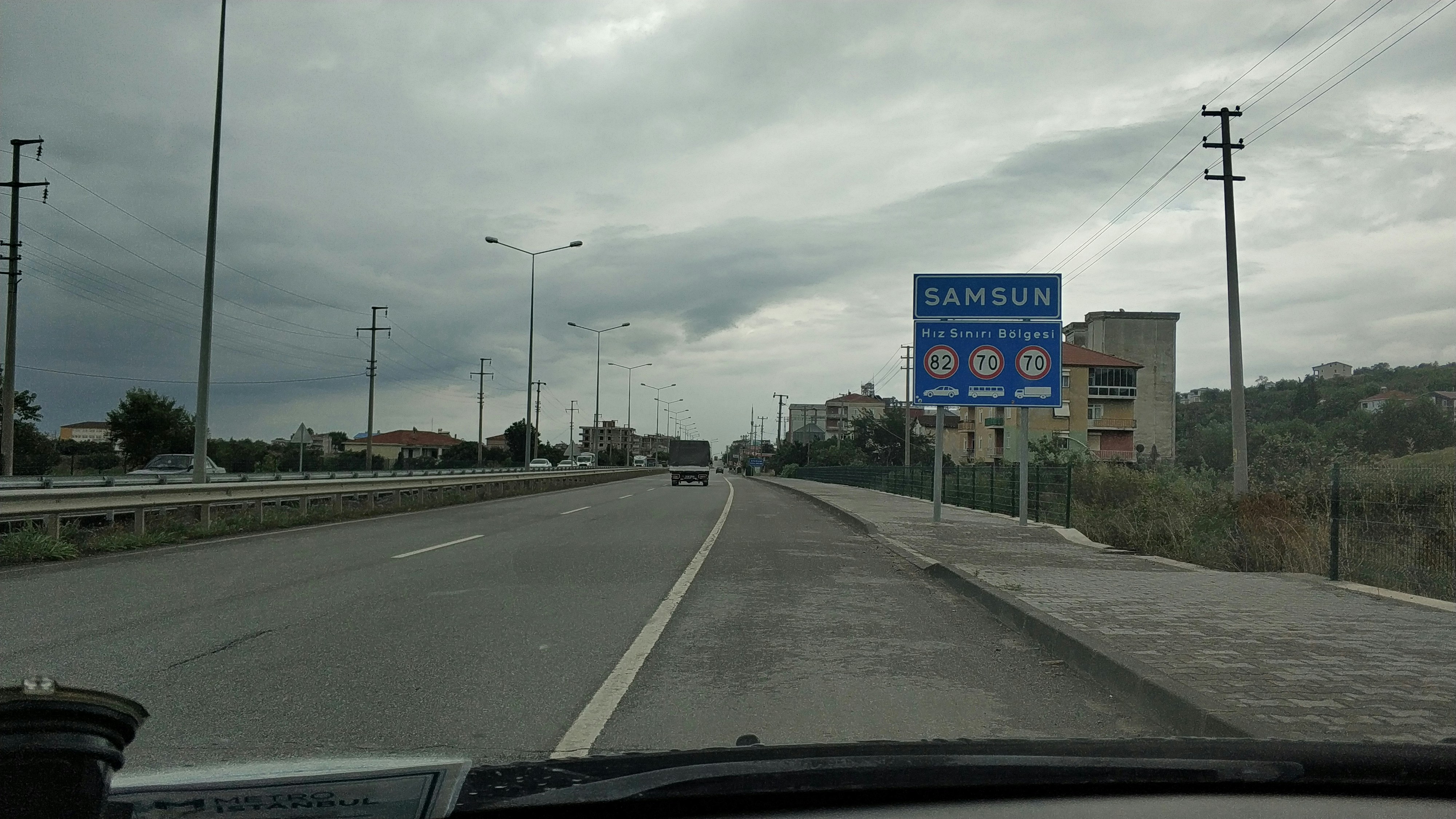 Car traveling on an empty road beneath a cloudy sky with visible road signs and power lines.