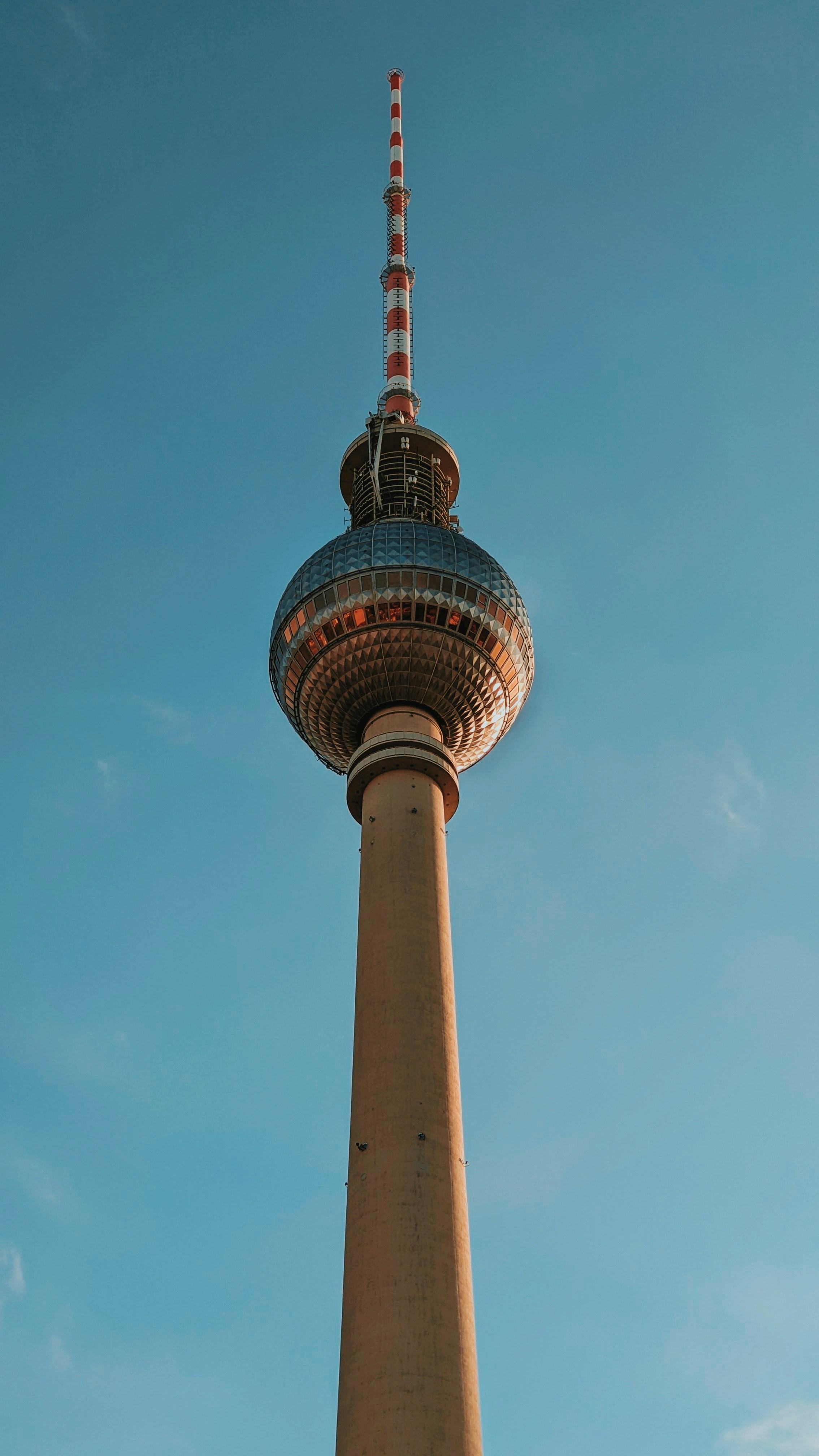 Berlin TV Tower rises against a clear blue sky, showcasing its iconic design and vibrant colors. The structure's details highlight its architectural significance.