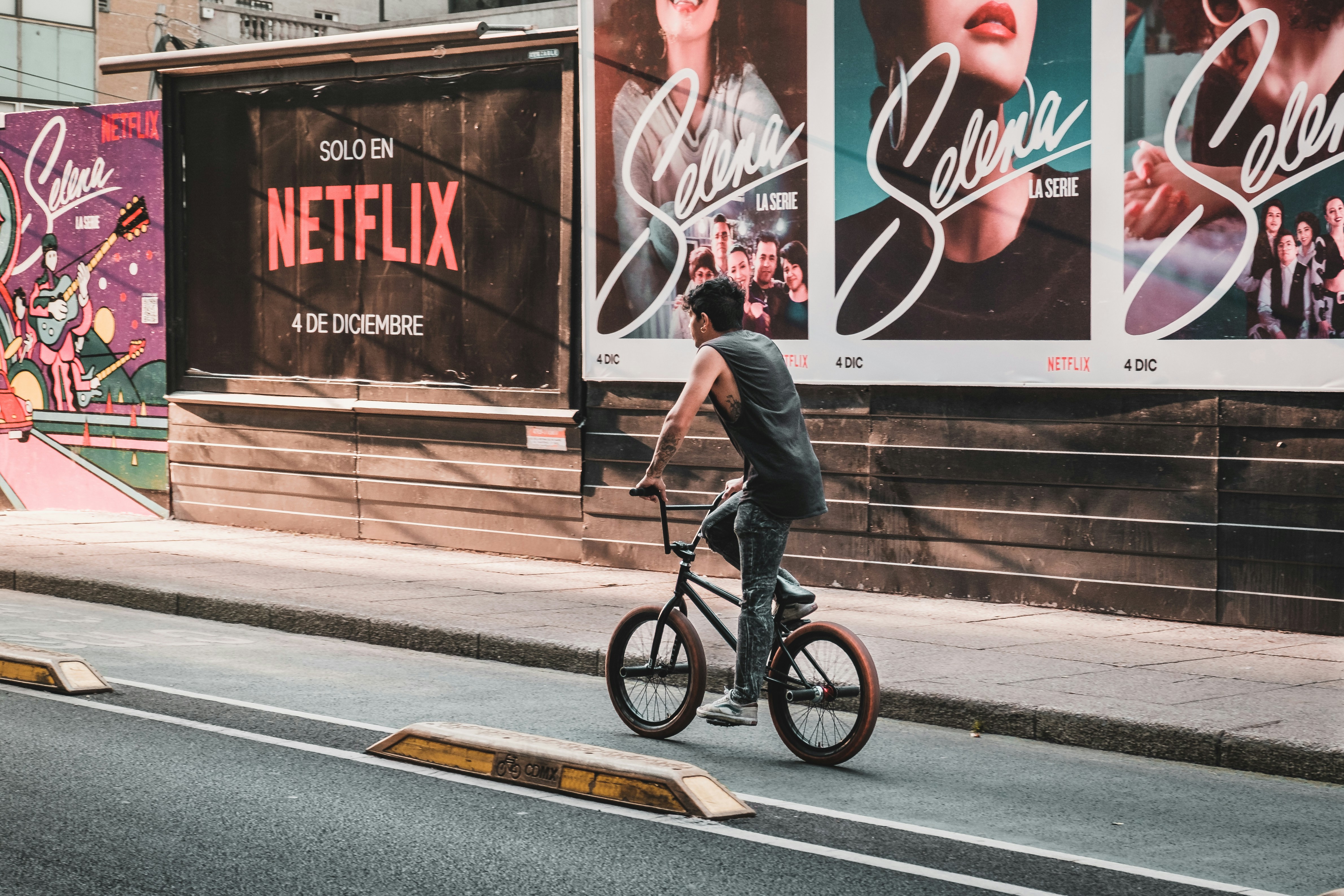 Bicyclist cruising past vibrant street billboards under a clear sky.