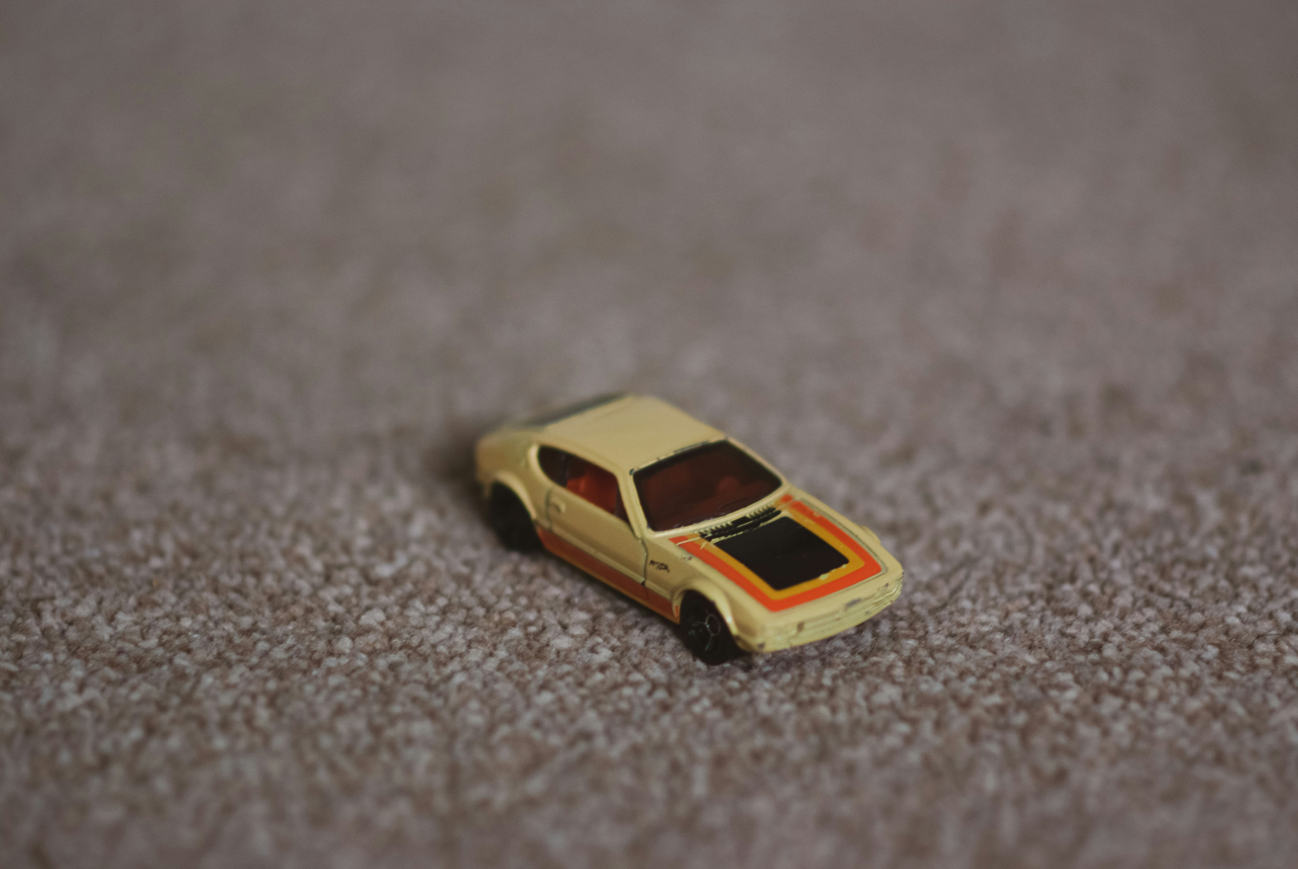 Yellow toy car with red and black accents resting on a soft carpet surface.