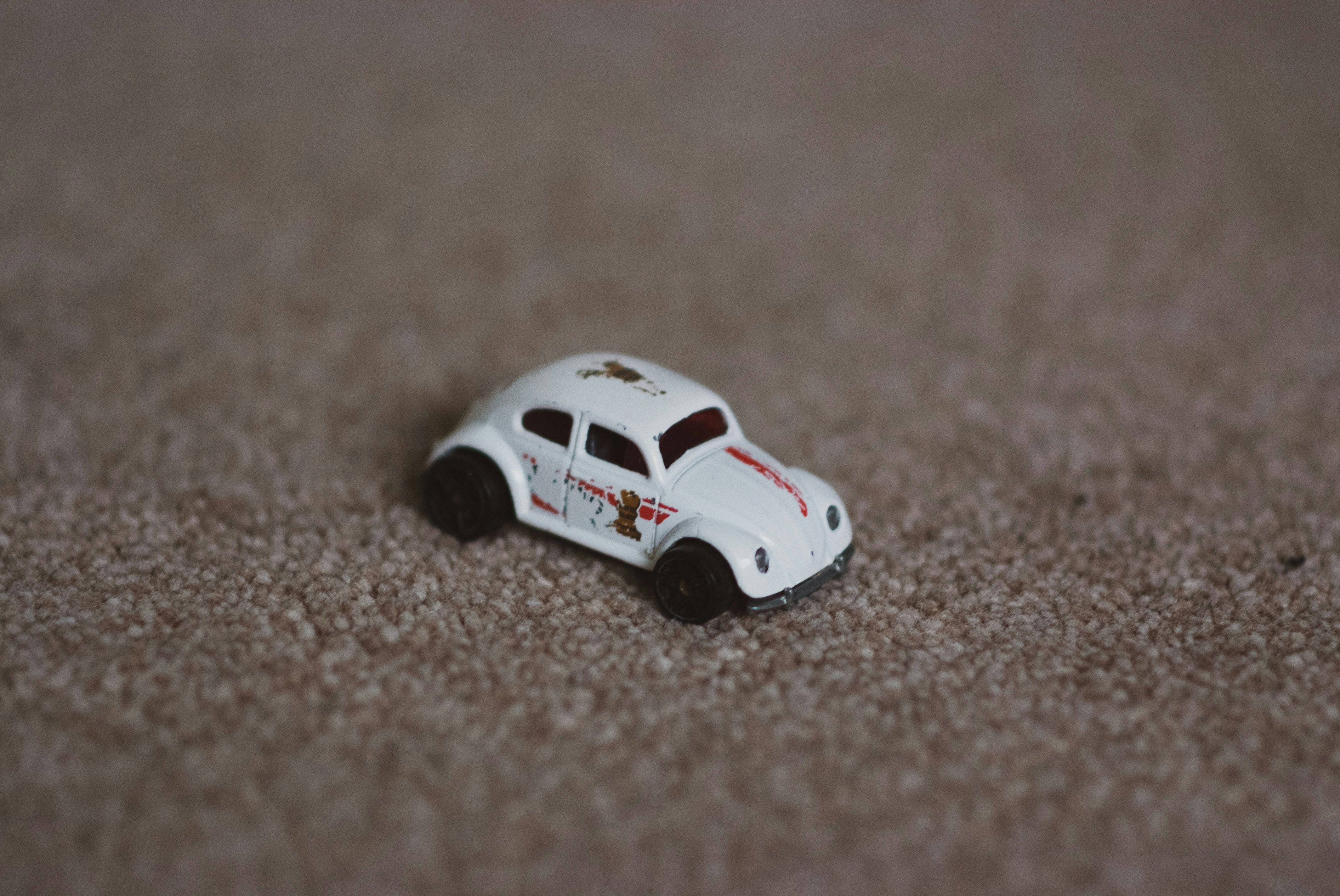 A miniature white toy van rests on coarse sand, with shallow depth of field blurring the background. The shot isolates the model to highlight its tiny details.