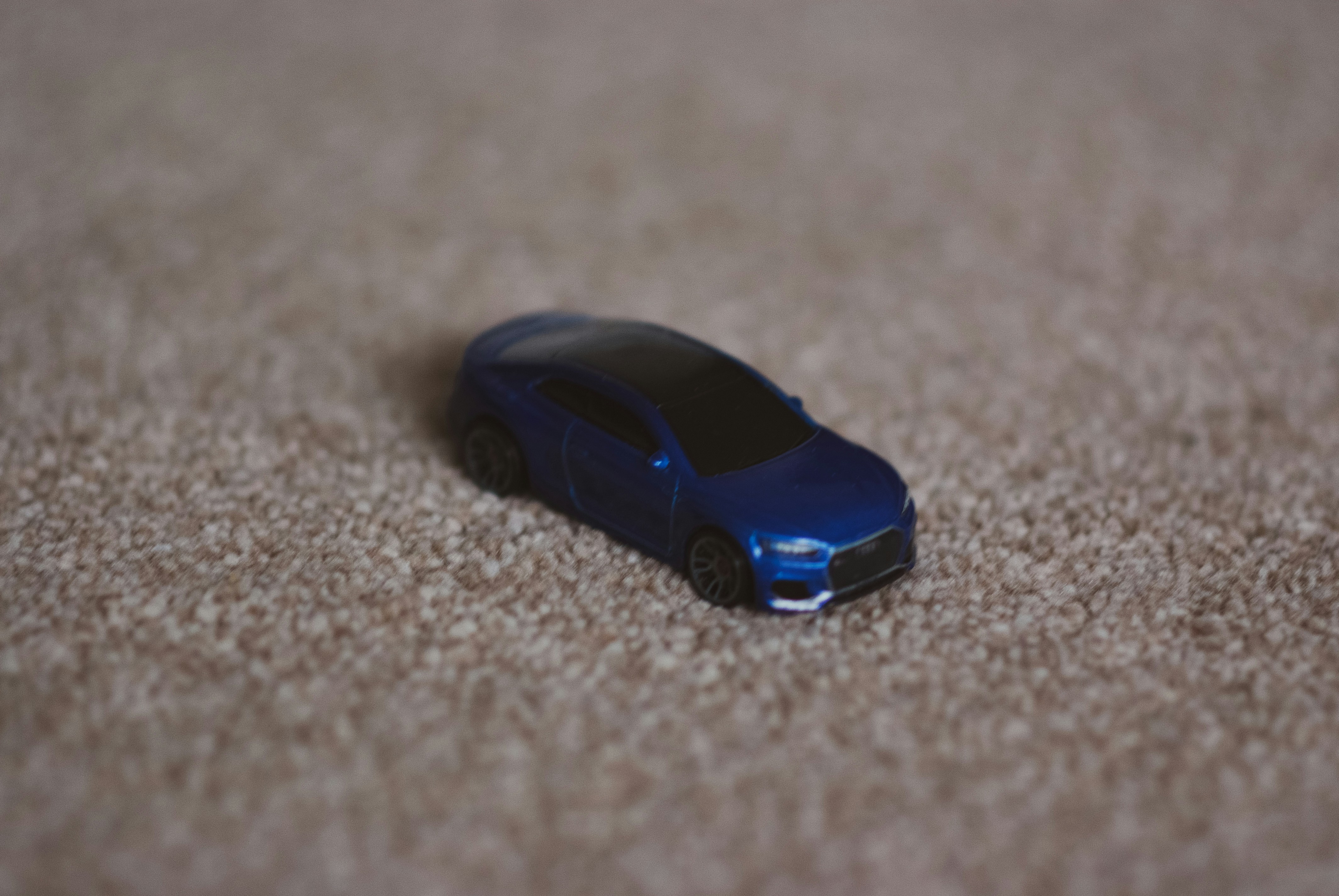 A detailed blue toy car resting on a textured carpet surface.