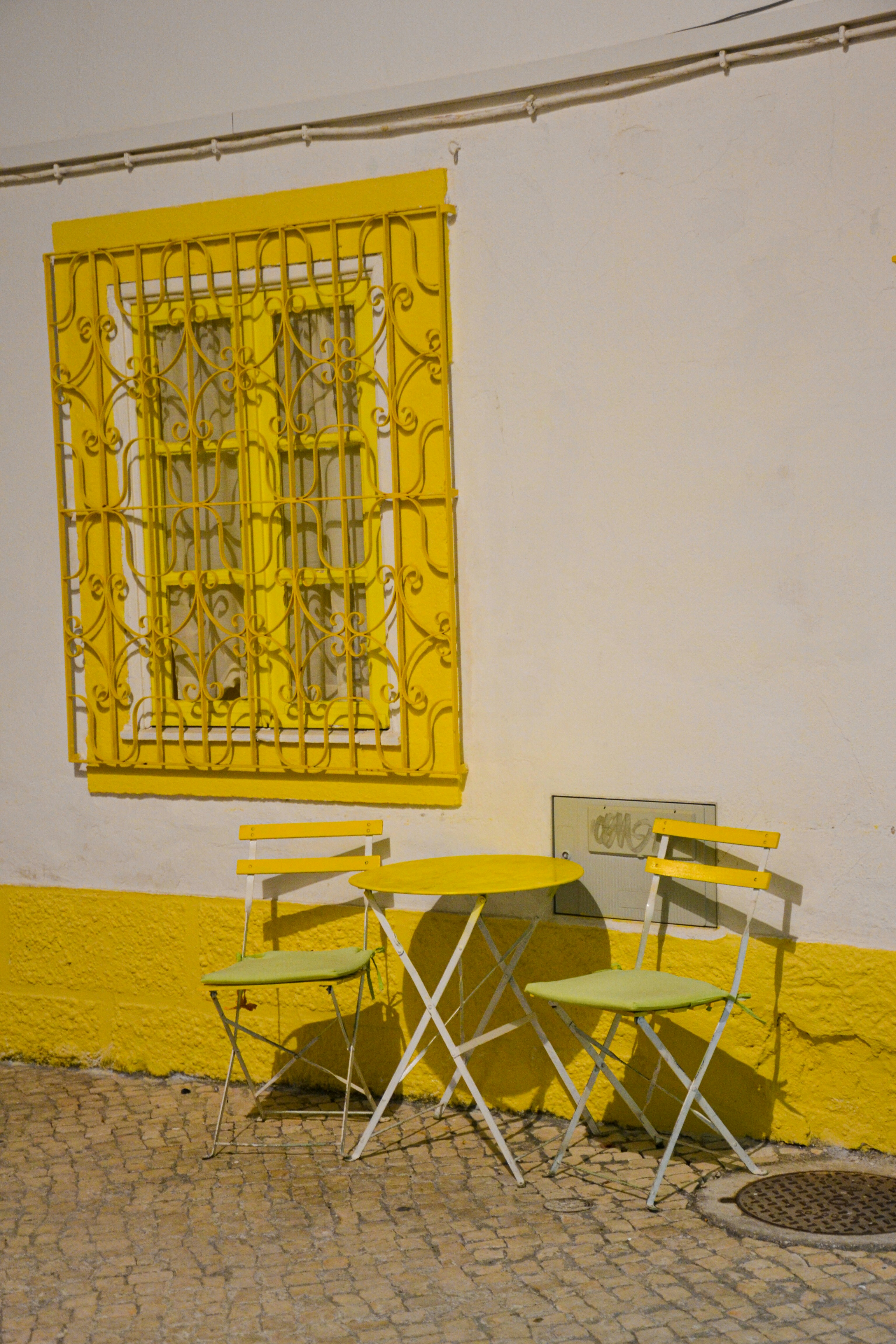 Yellow window and furniture against a white wall with cobblestone street.