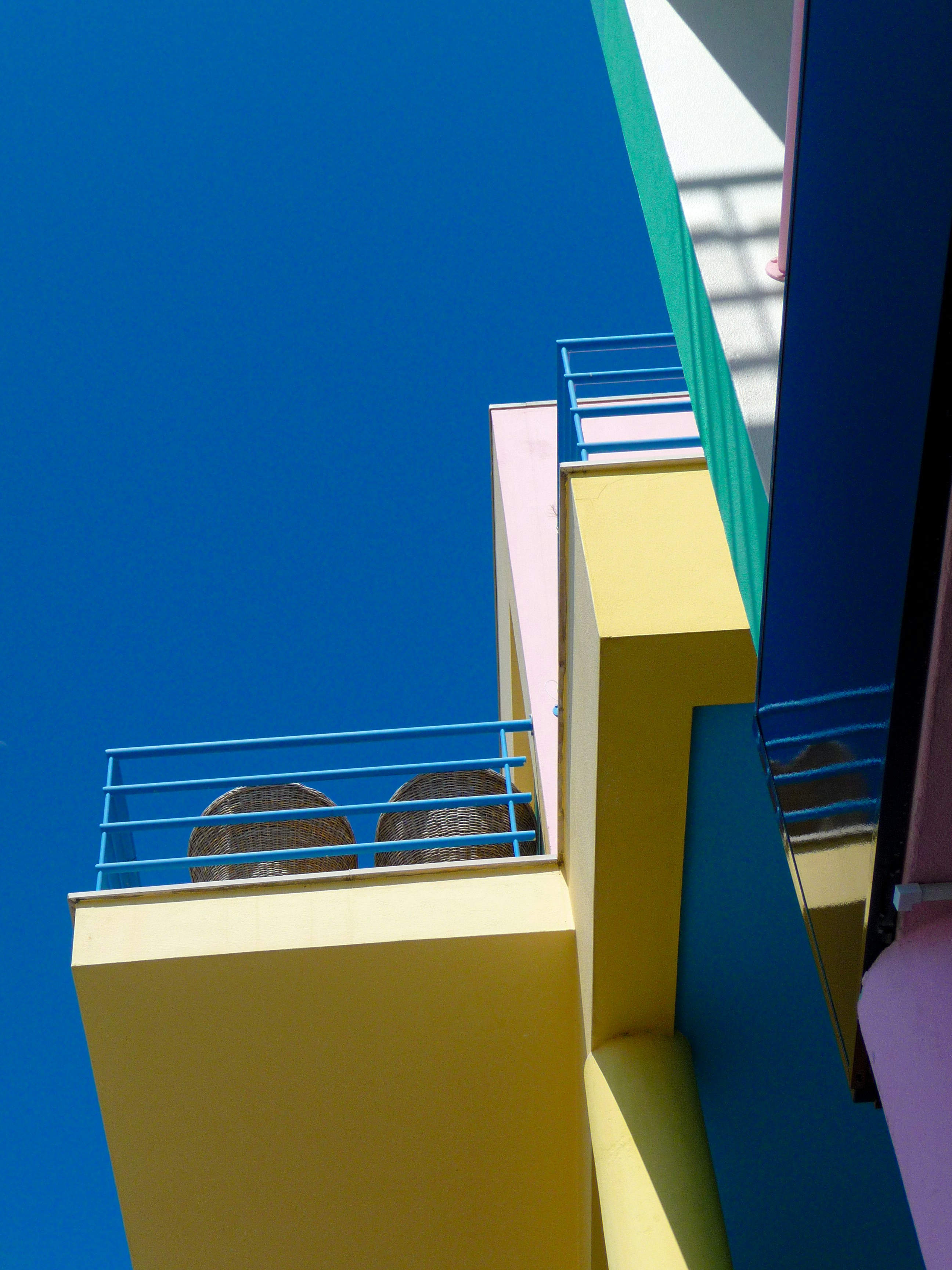 Vibrant balconies with blue railings overlook a clear blue sky, showcasing a unique architectural design. The interplay of colors creates a lively urban scene.