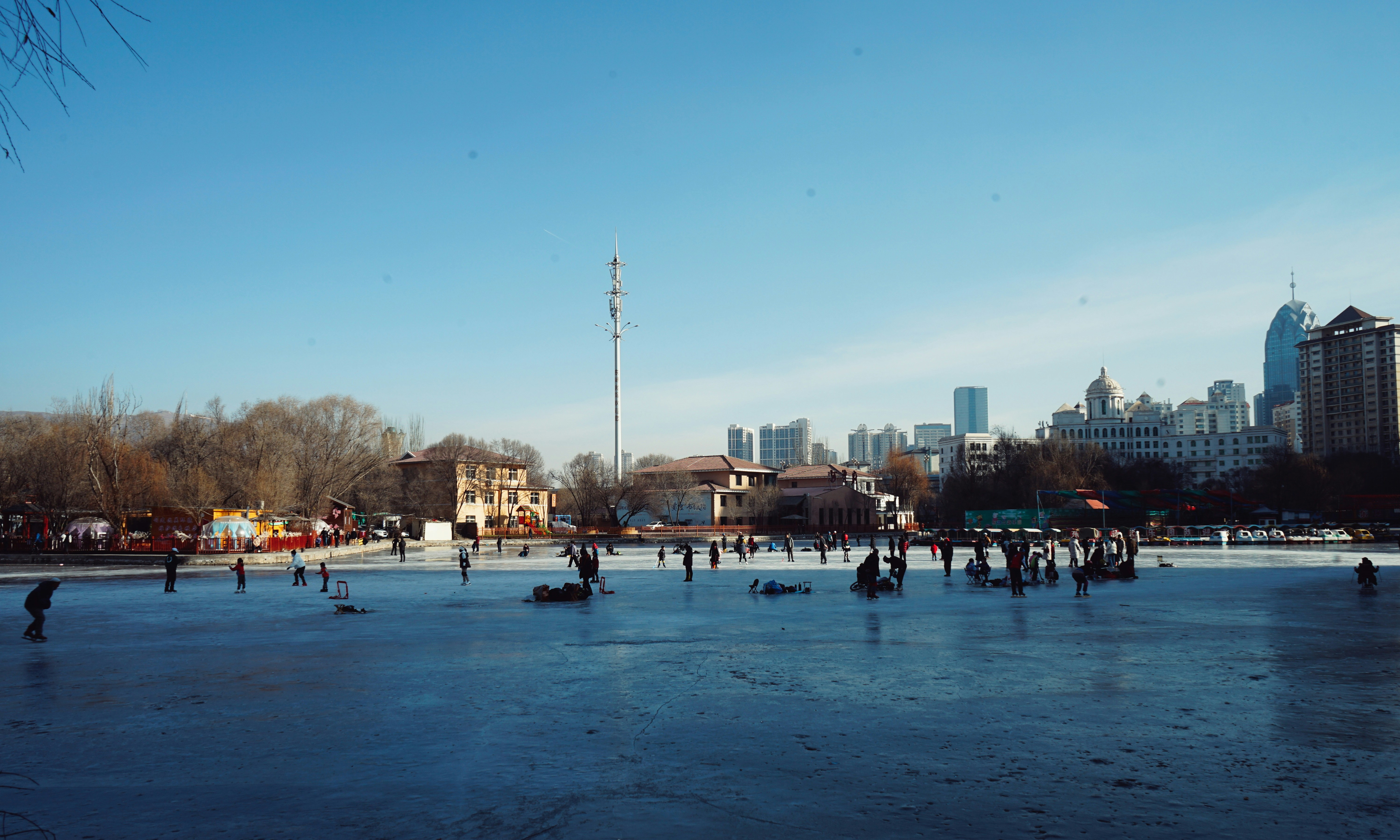 Skaters enjoying a frozen pond surrounded by urban architecture on a clear winter day.