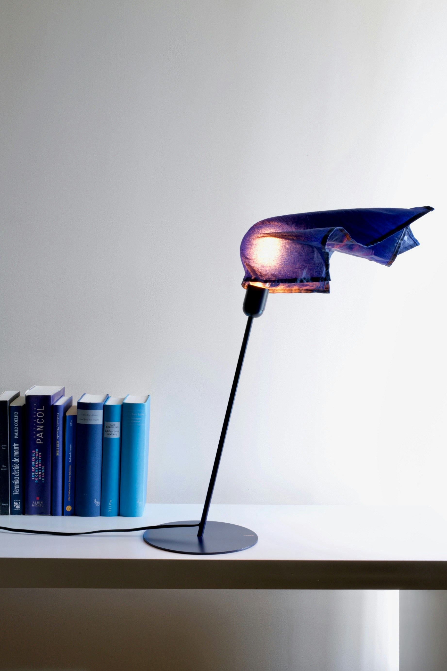 Purple Lampshade on a Slim Desk Lamp Beside a Row of Blue Books