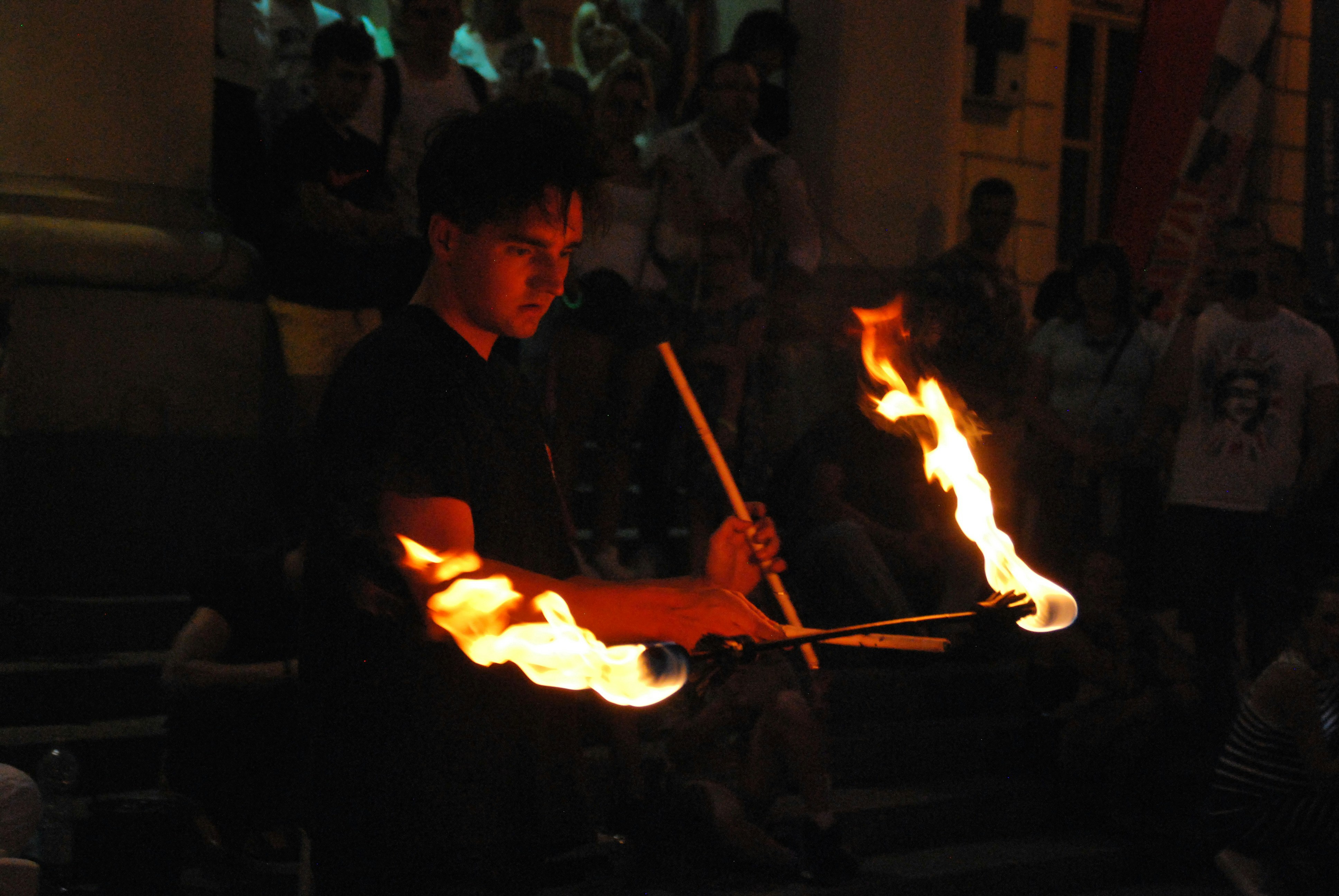 Performer skillfully twirls flaming batons in a dimly lit outdoor setting.