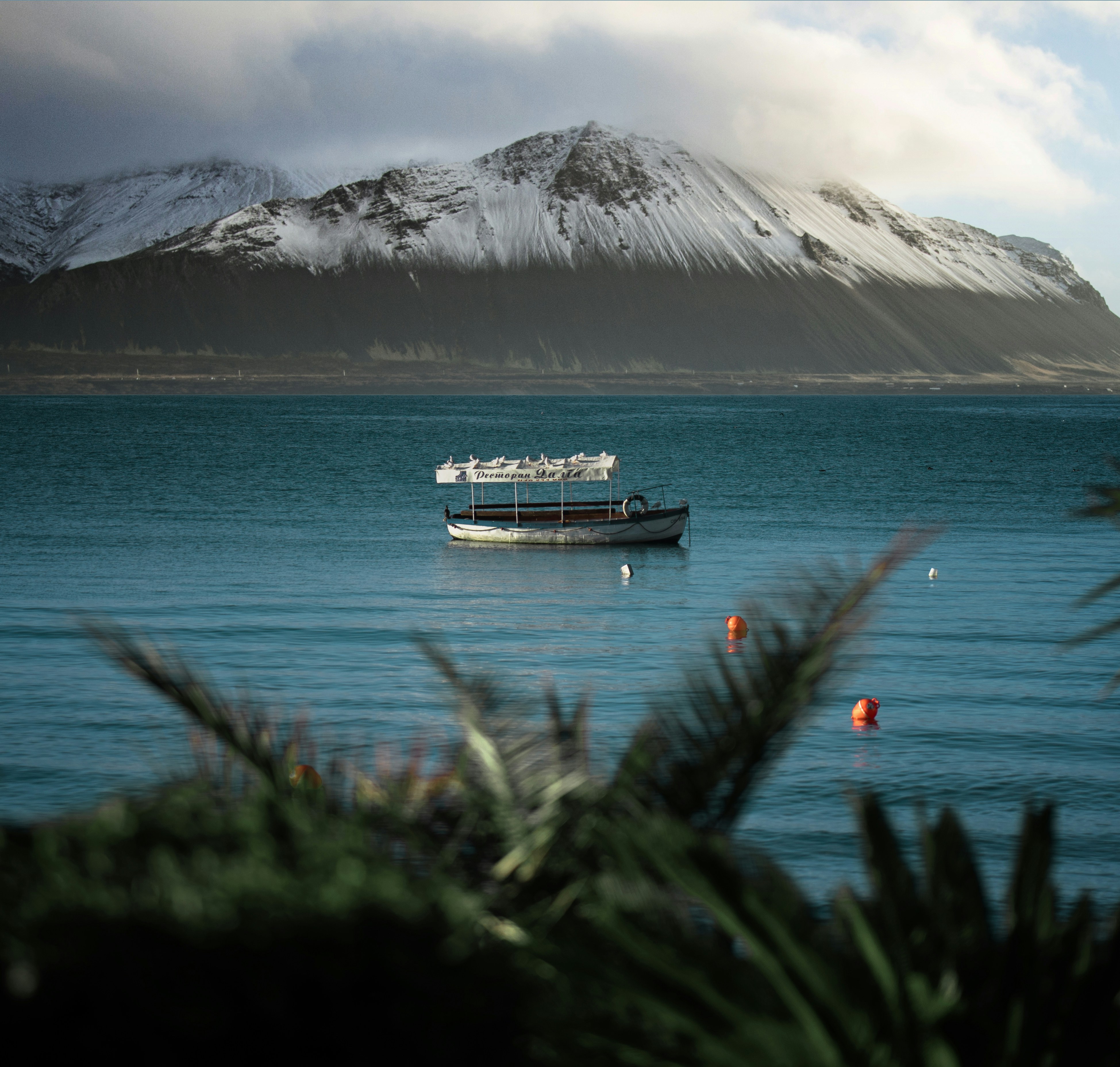 A small boat gently floats on tranquil waters, framed by majestic snow-capped mountains under a clear sky.
