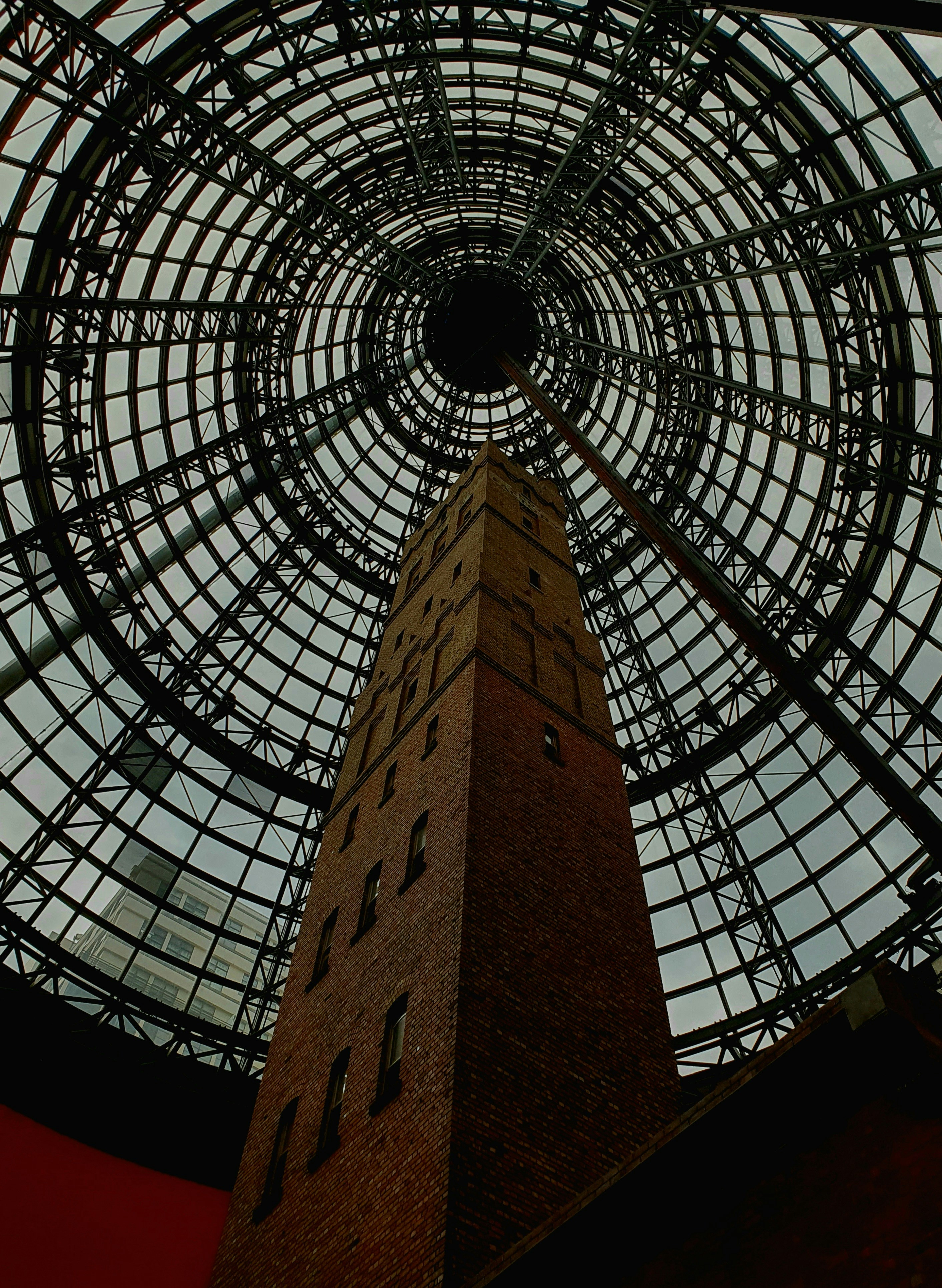Historic brick tower rising beneath a circular glass dome, showcasing intricate architectural details and modern contrasts.